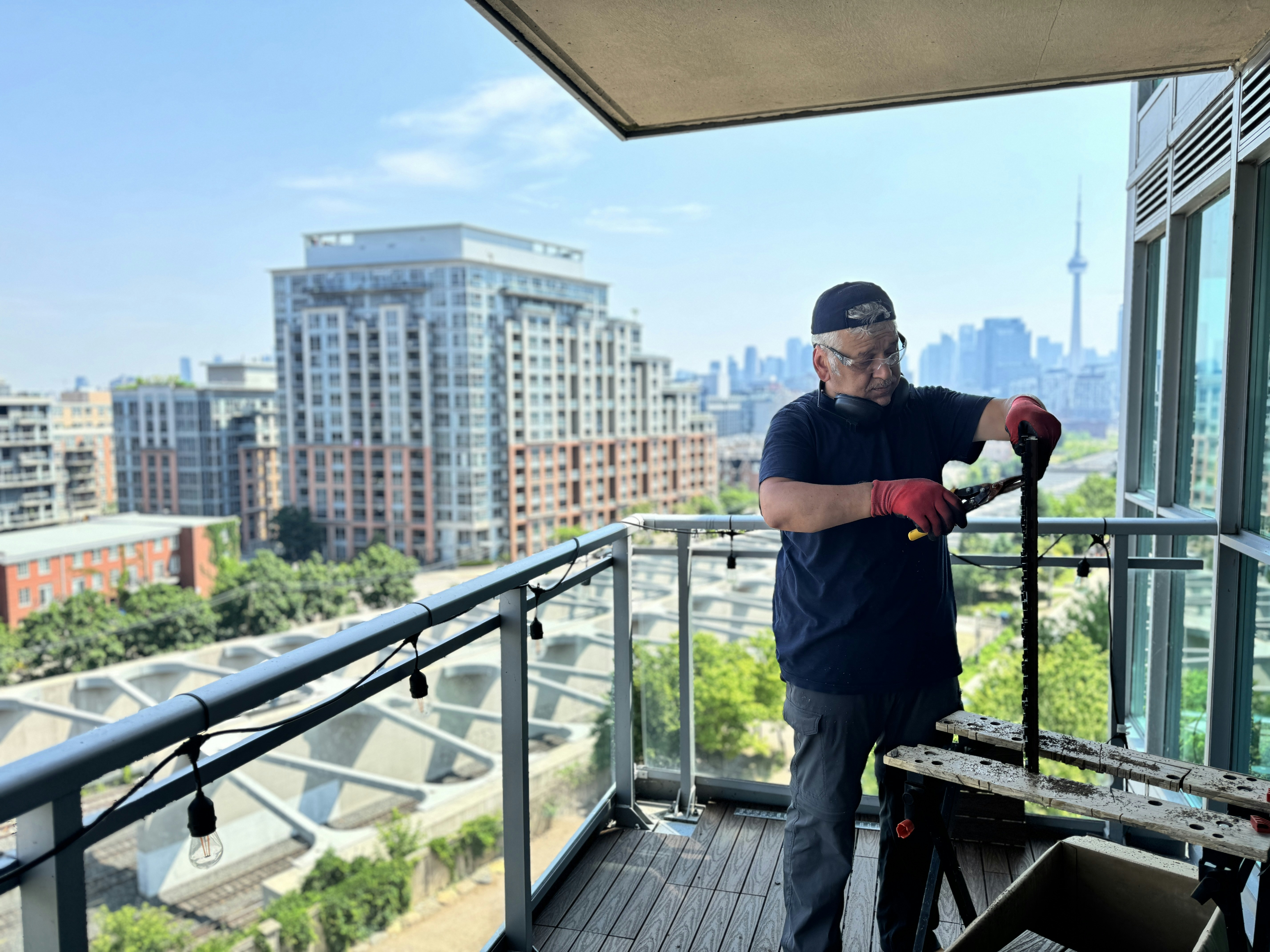 Person working on a balcony with city skyline in the background under a clear blue sky.