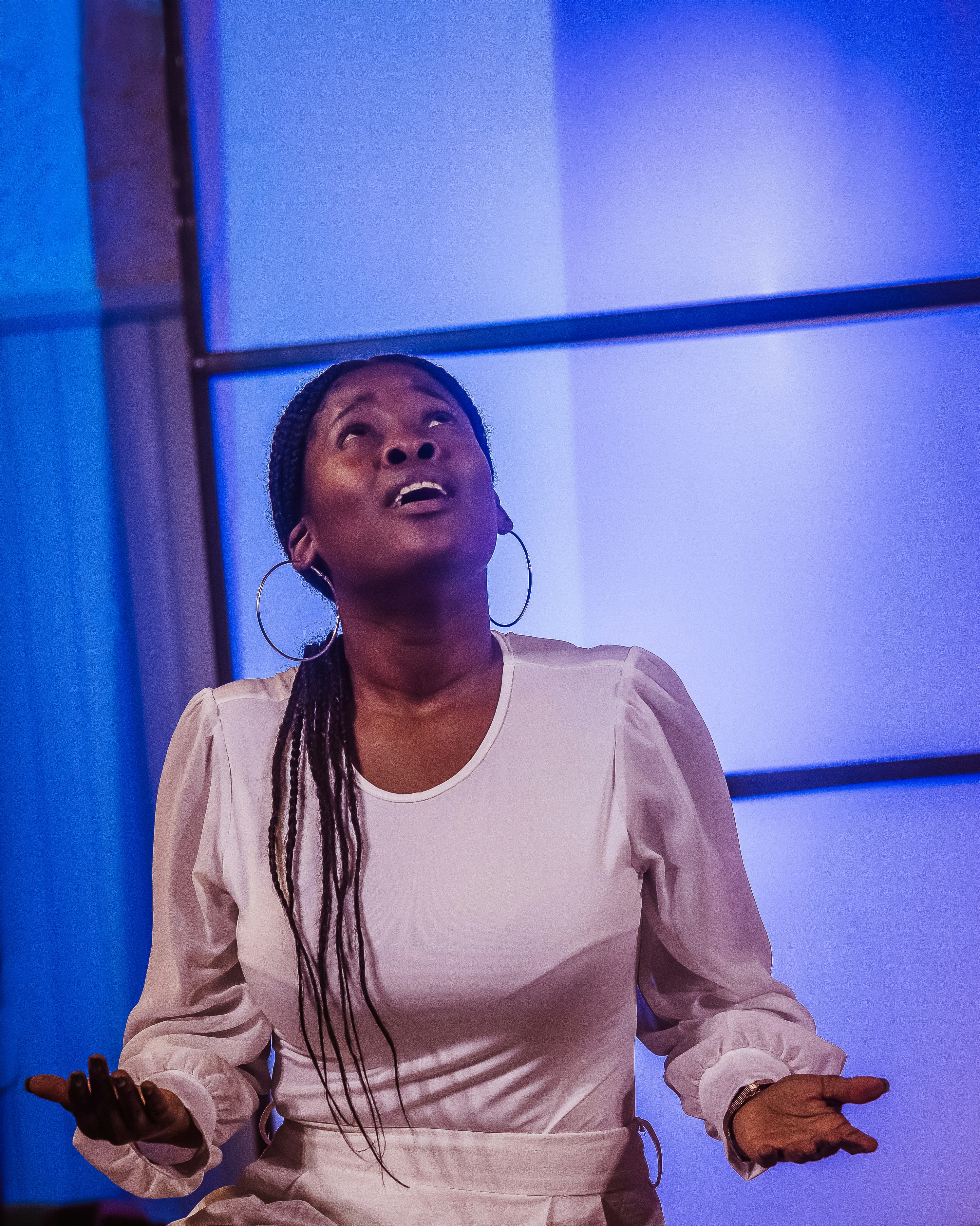 Person looking upward, bathed in soft blue light, wearing a white outfit.
