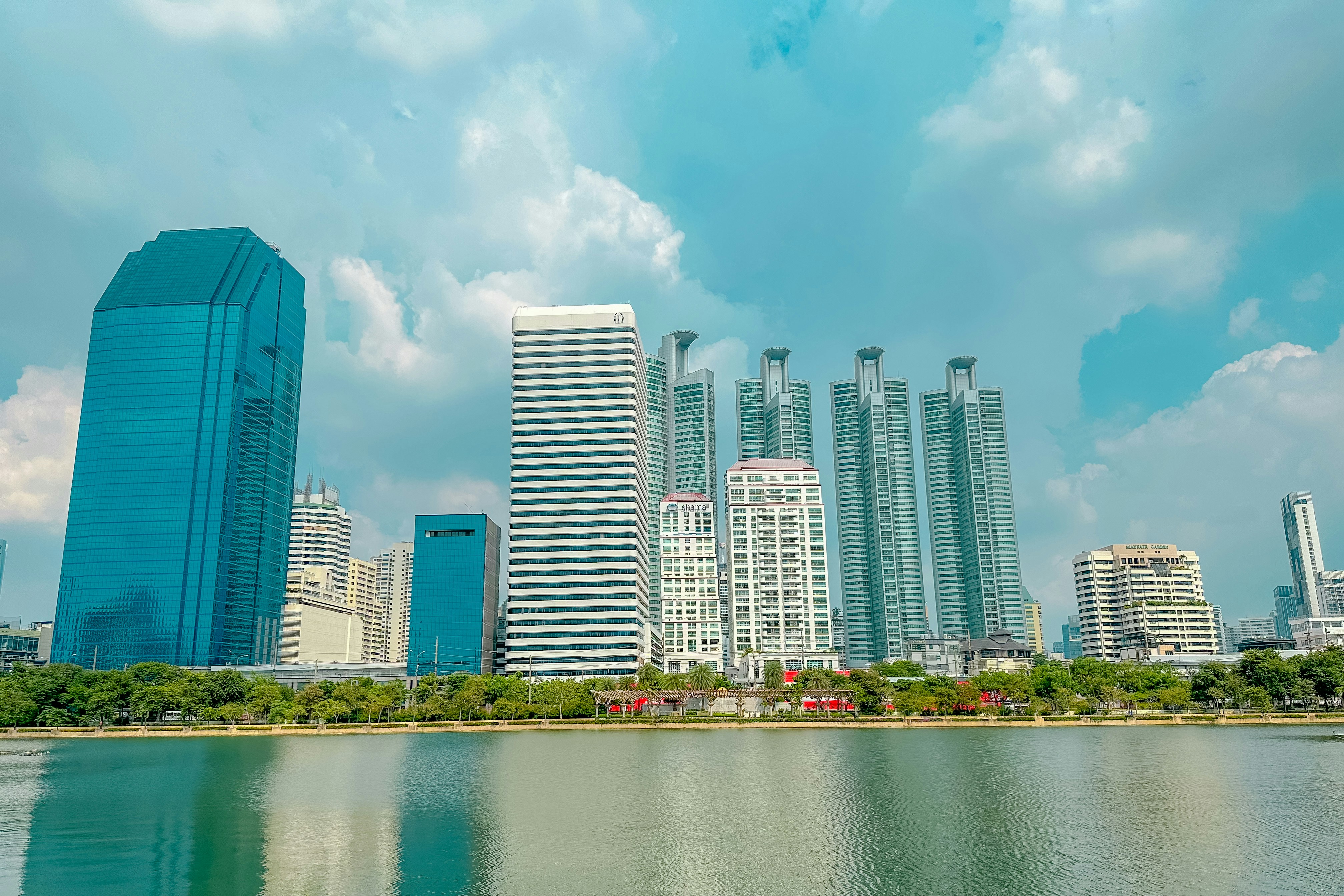 Tall skyscrapers along a tranquil lake under a partly cloudy sky.