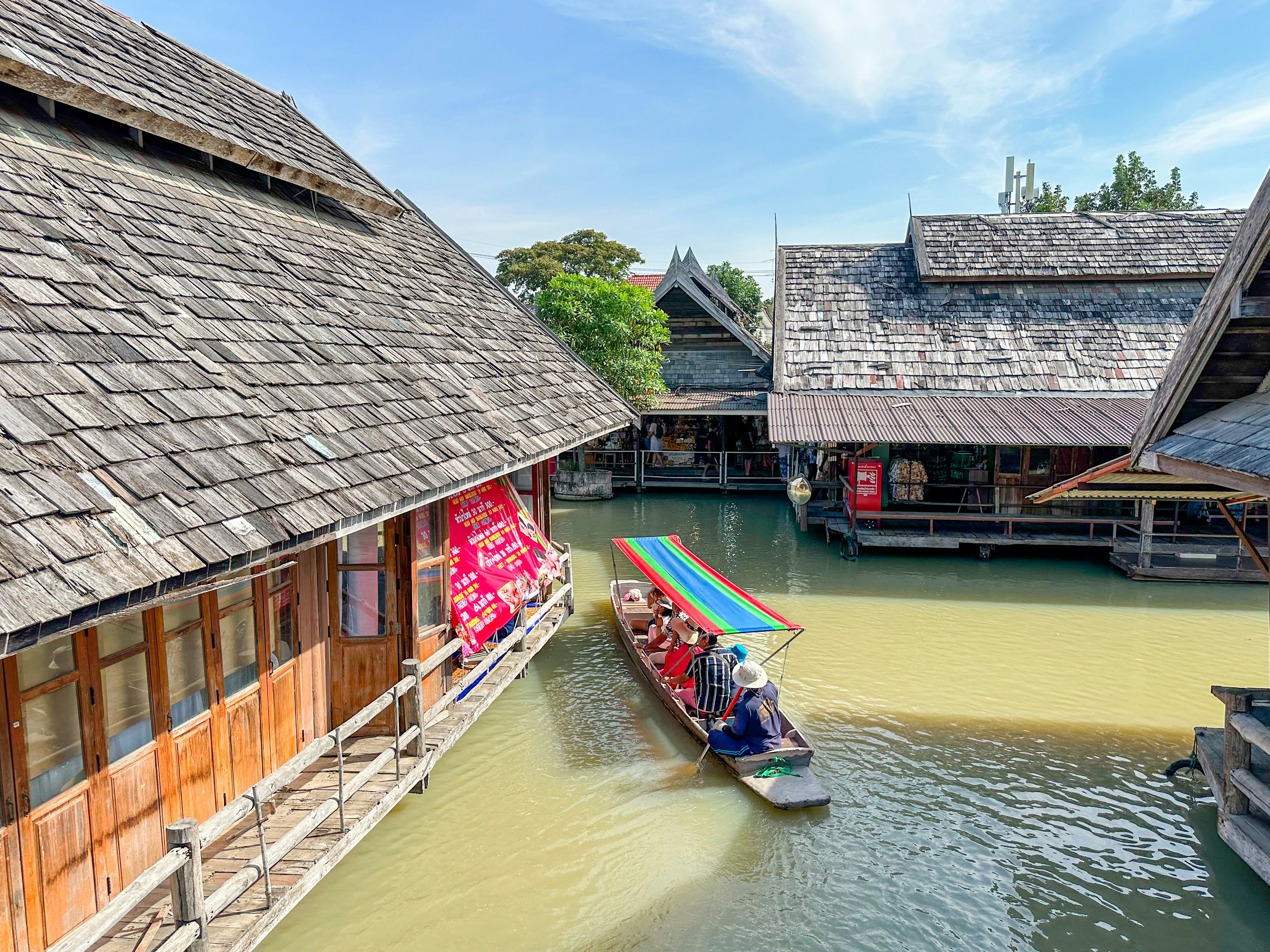 Wooden buildings surround a narrow canal with a boat carrying tourists under a clear blue sky.