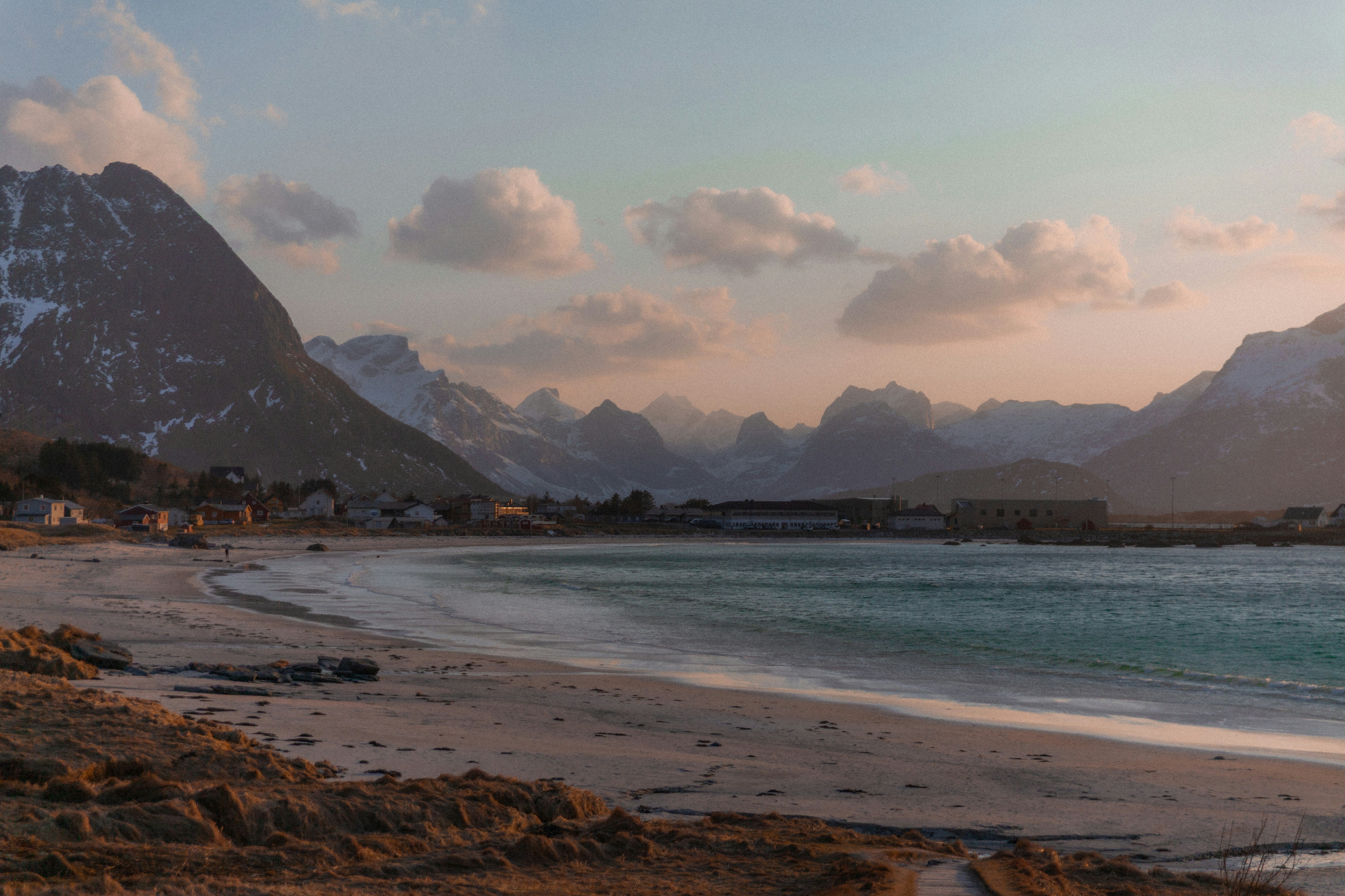Coastal landscape with mountains and calm sea under a soft, pastel sky.