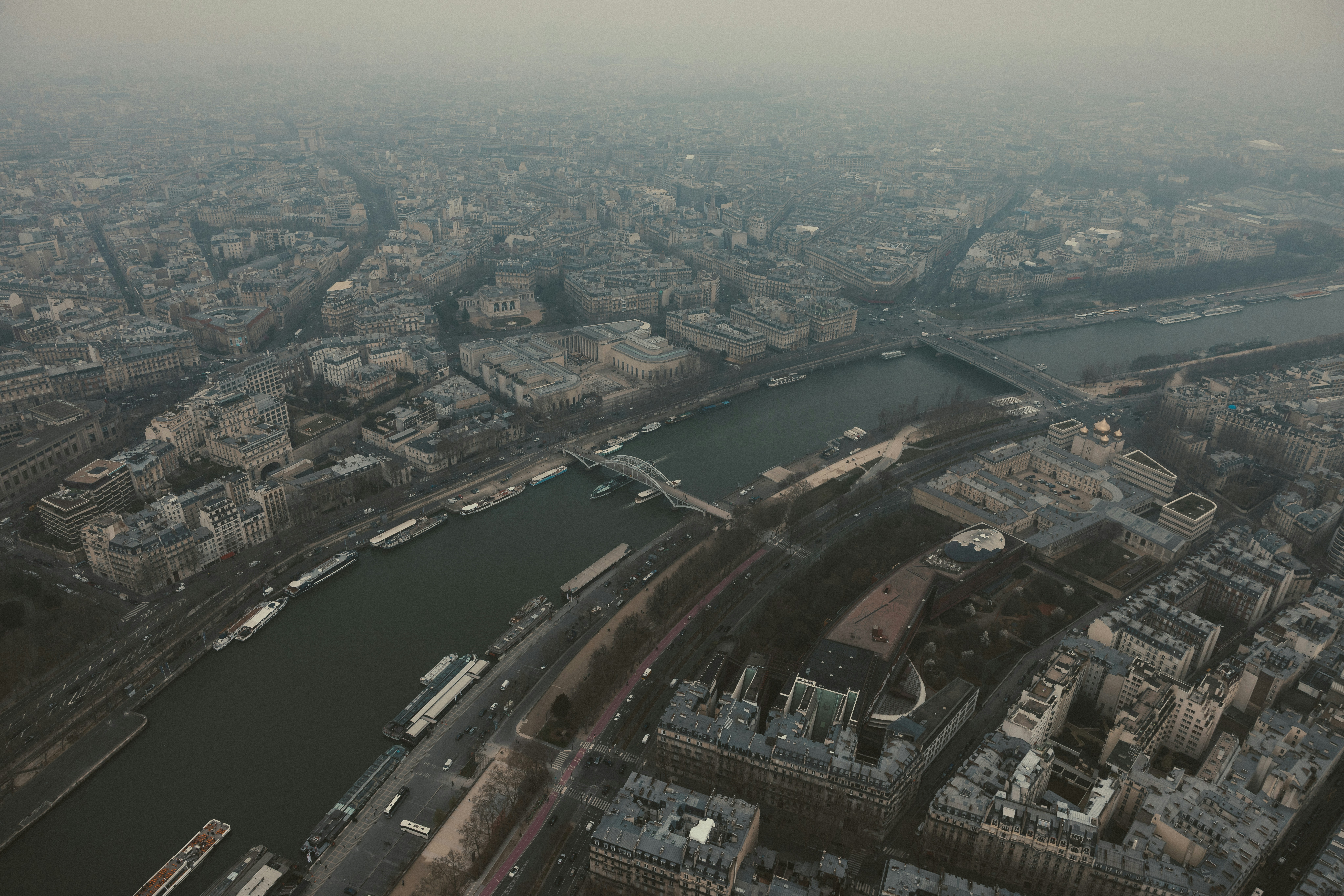 Aerial view of a sprawling cityscape shrouded in mist, with a winding river cutting through dense urban architecture.