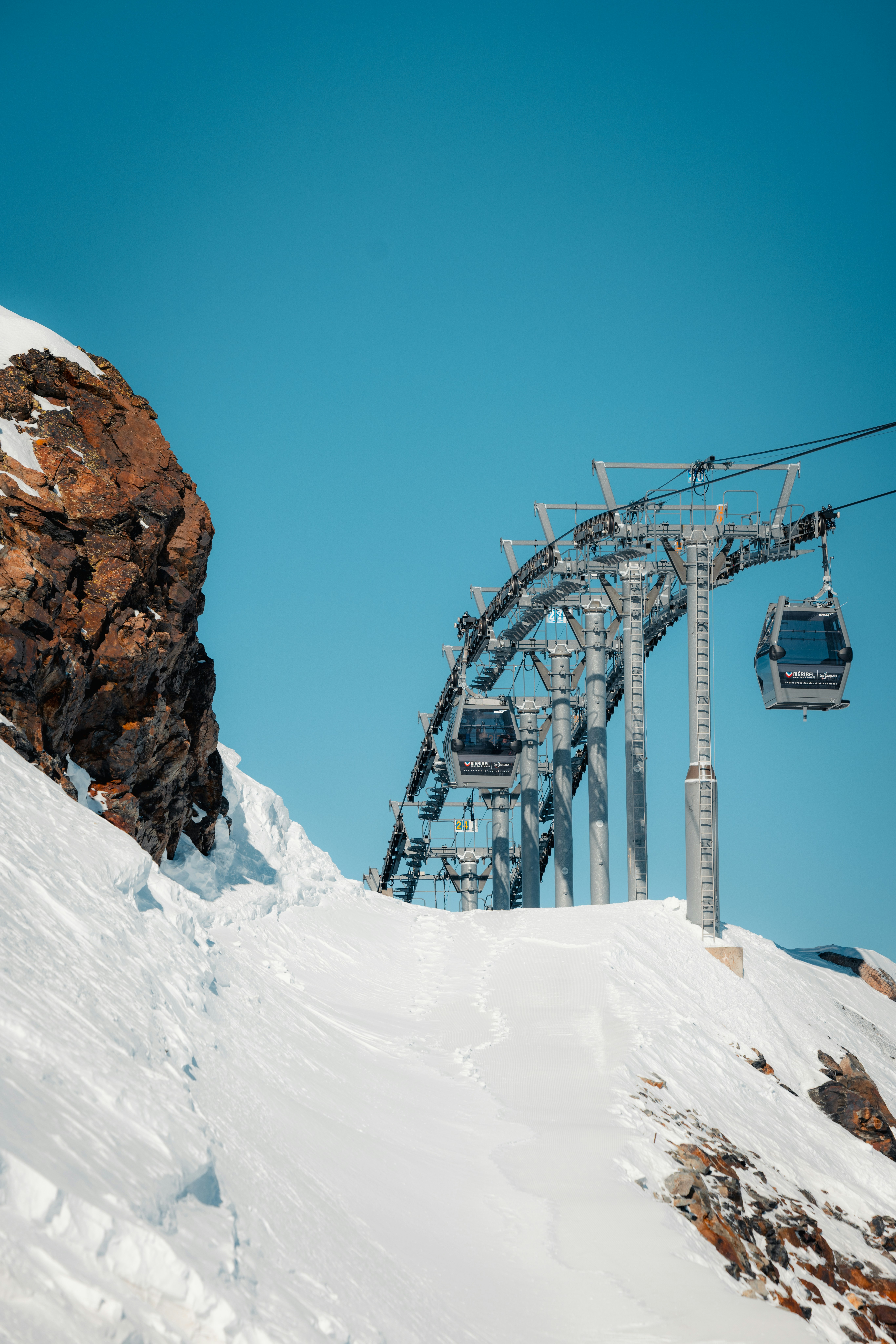 Cable cars ascend snowy mountains under a blue sky.