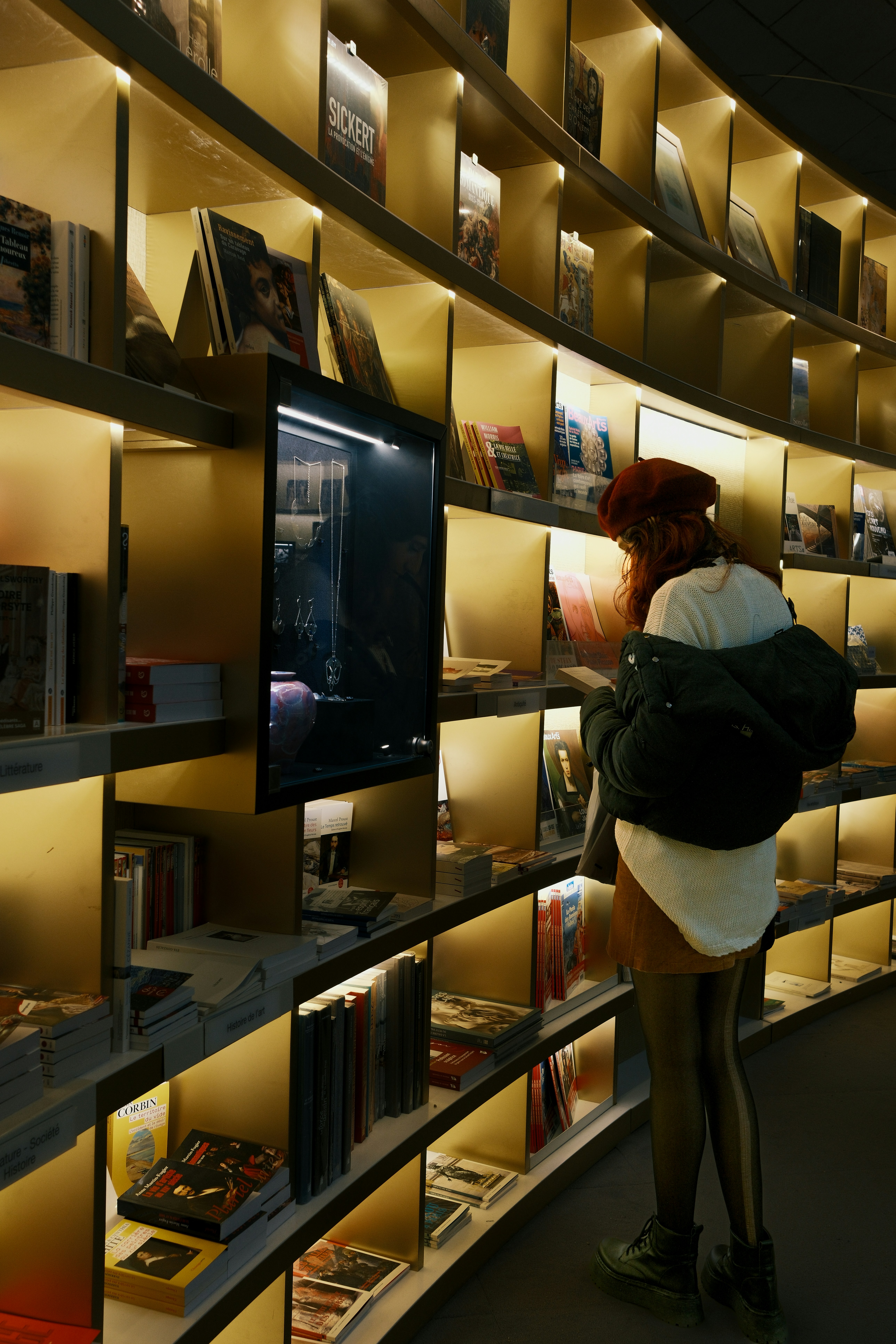 A person browses books in a lit bookstore. photo – Free Building Image ...