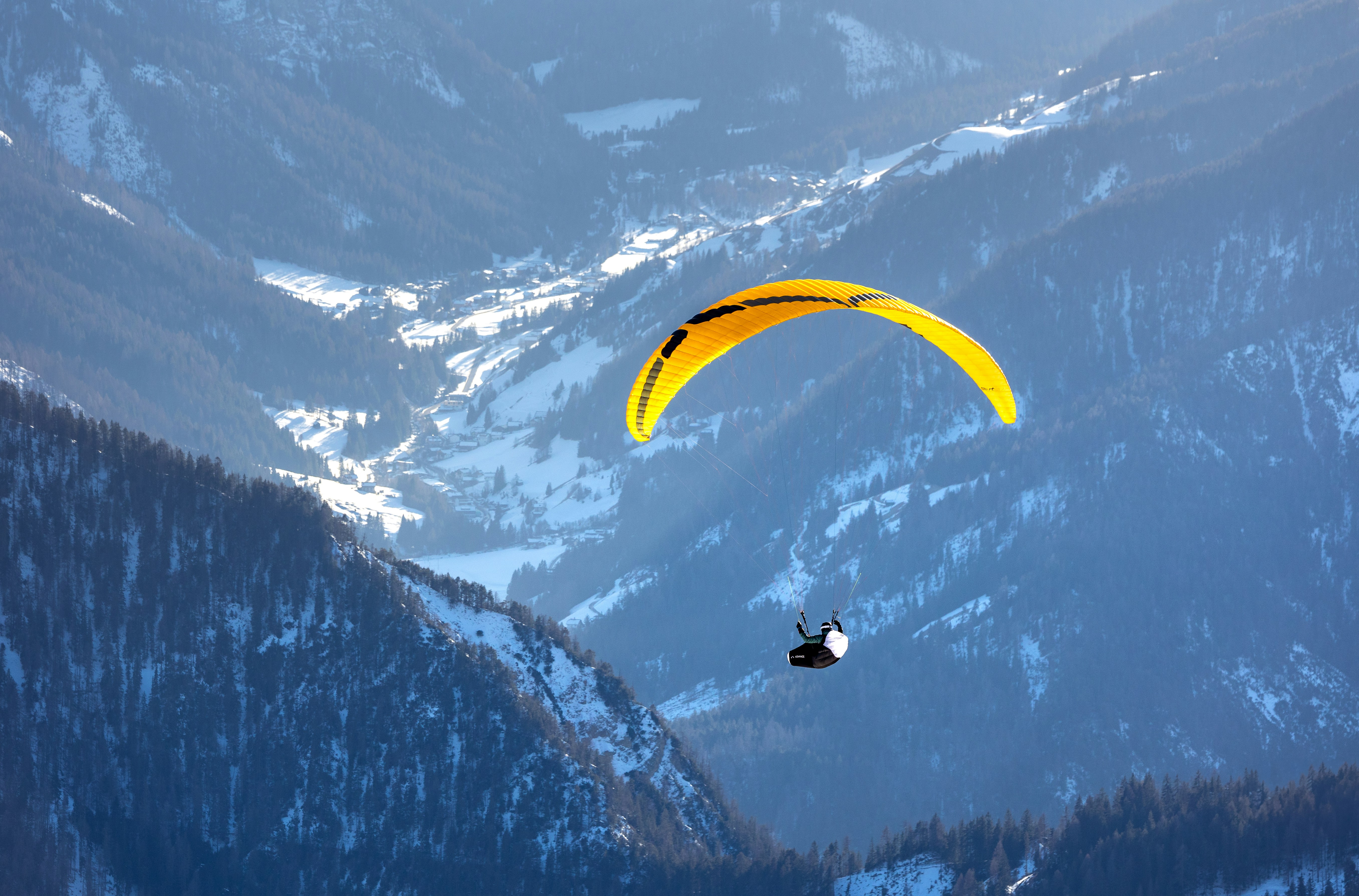 A paraglider soars over snowy mountains. photo – Free Human Image on ...