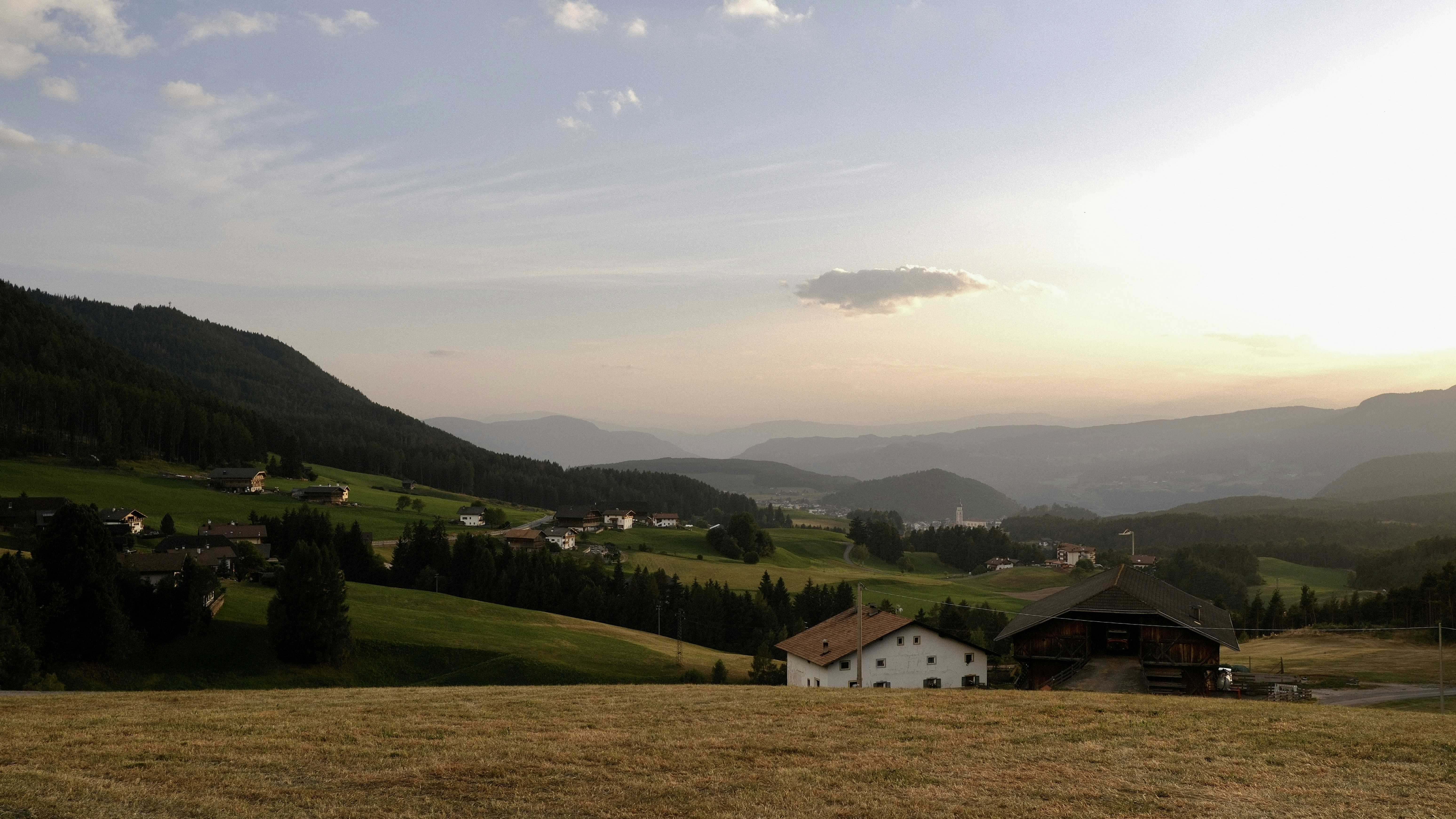 Rolling hills and scattered farmhouses under a soft evening sky.