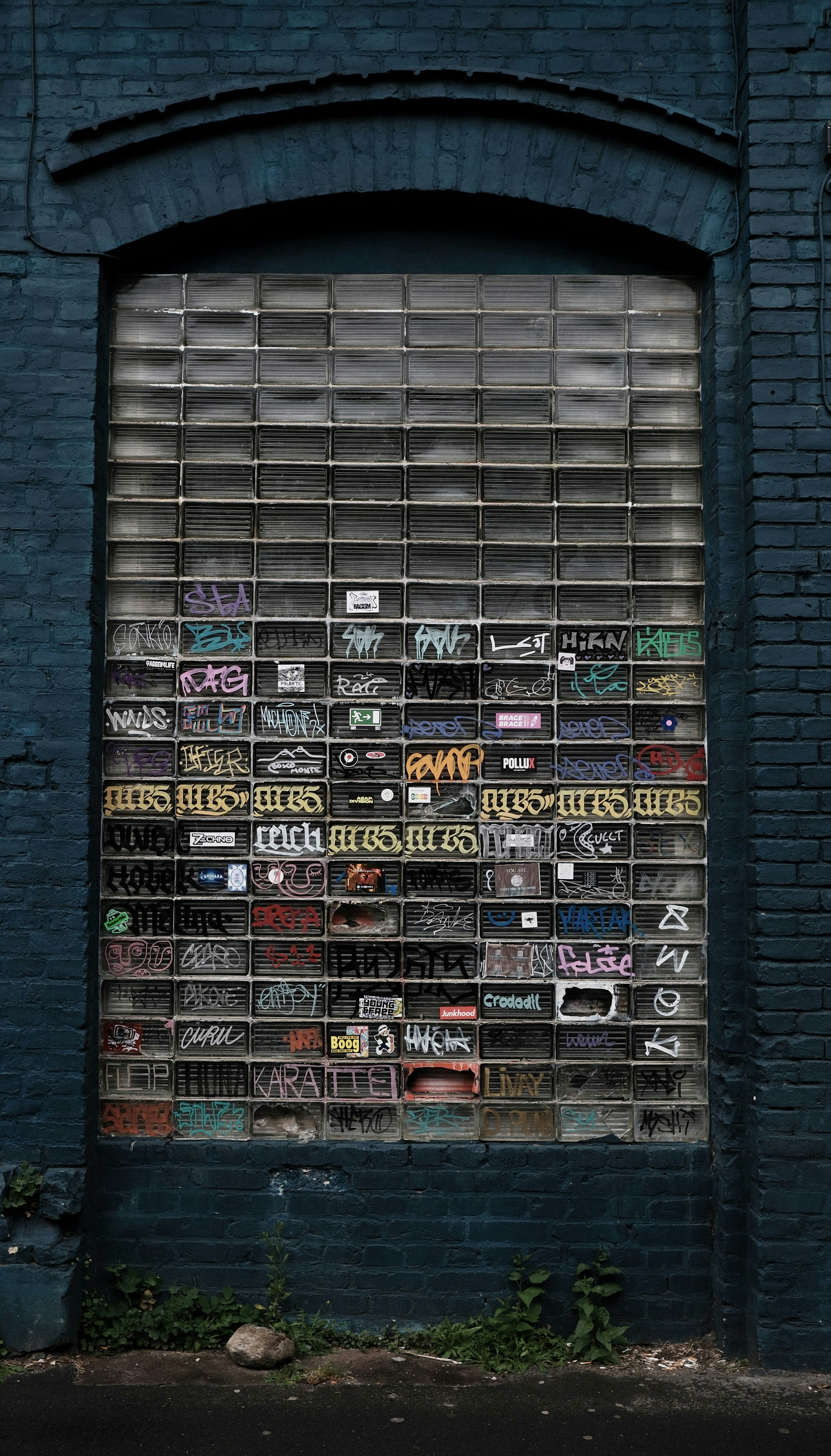 Graffiti-covered glass blocks within a blue brick wall.