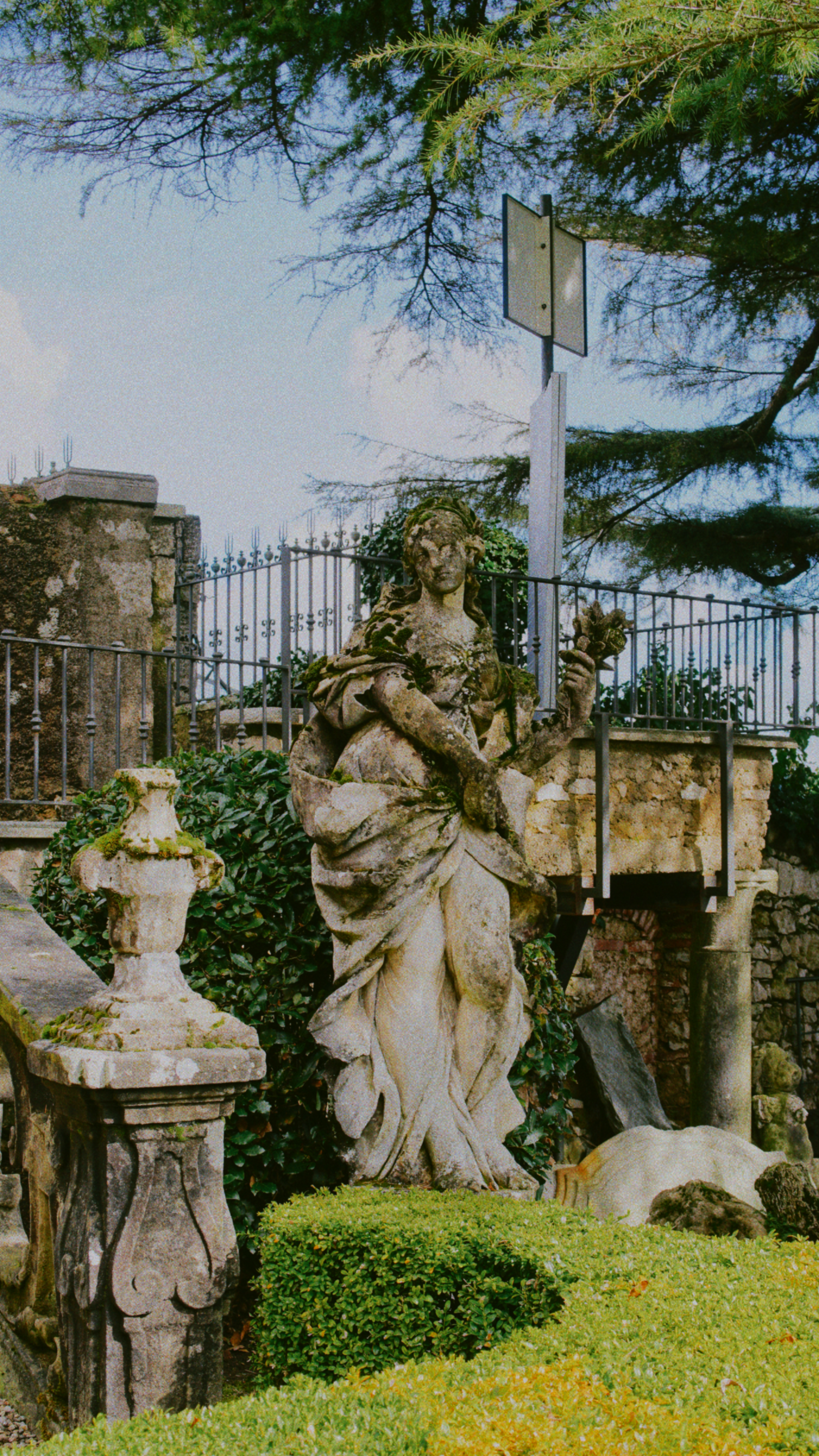 Weathered stone statue surrounded by greenery in a historic garden setting.