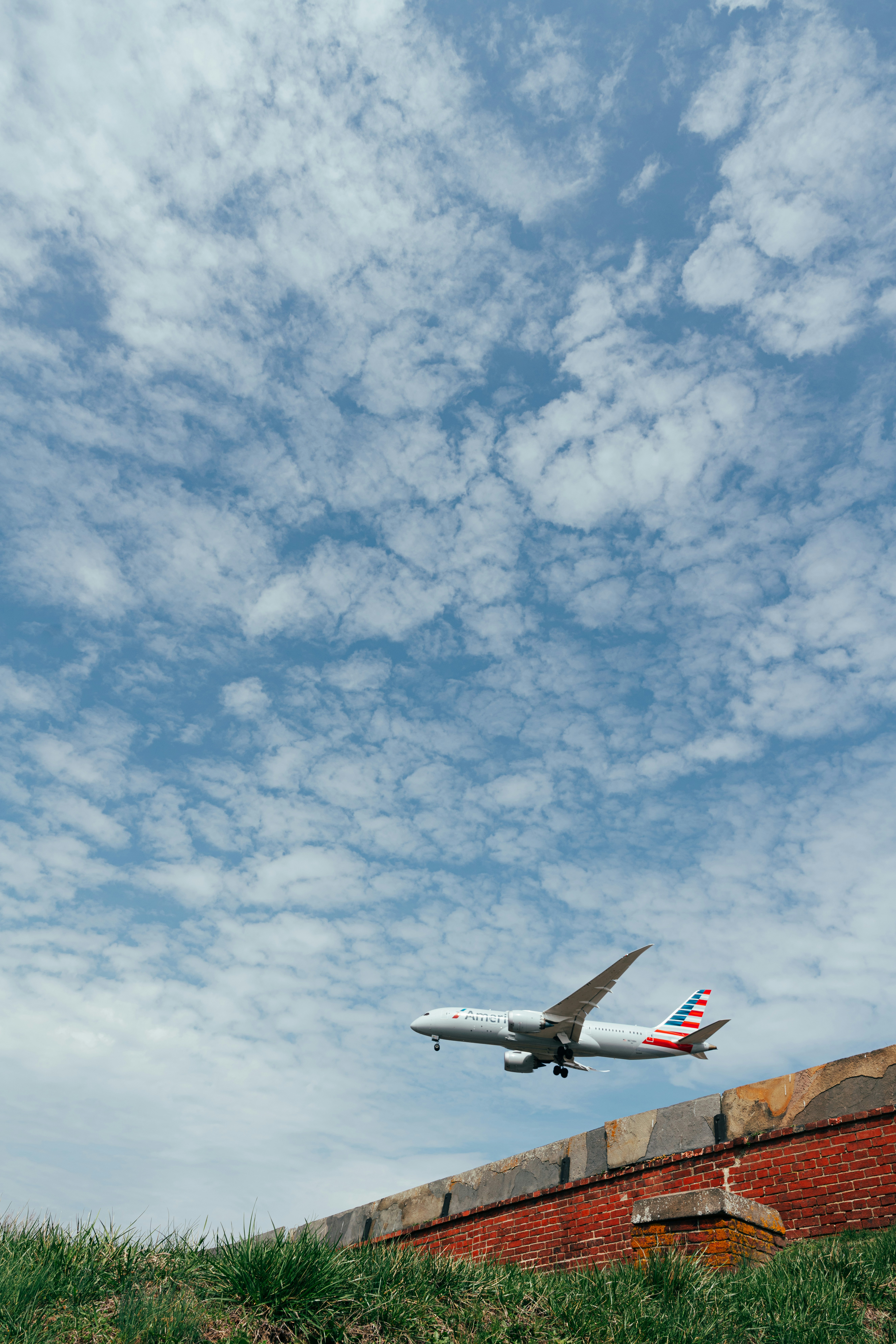 Airplane flies over a brick wall under a cloudy sky. photo – Free ...