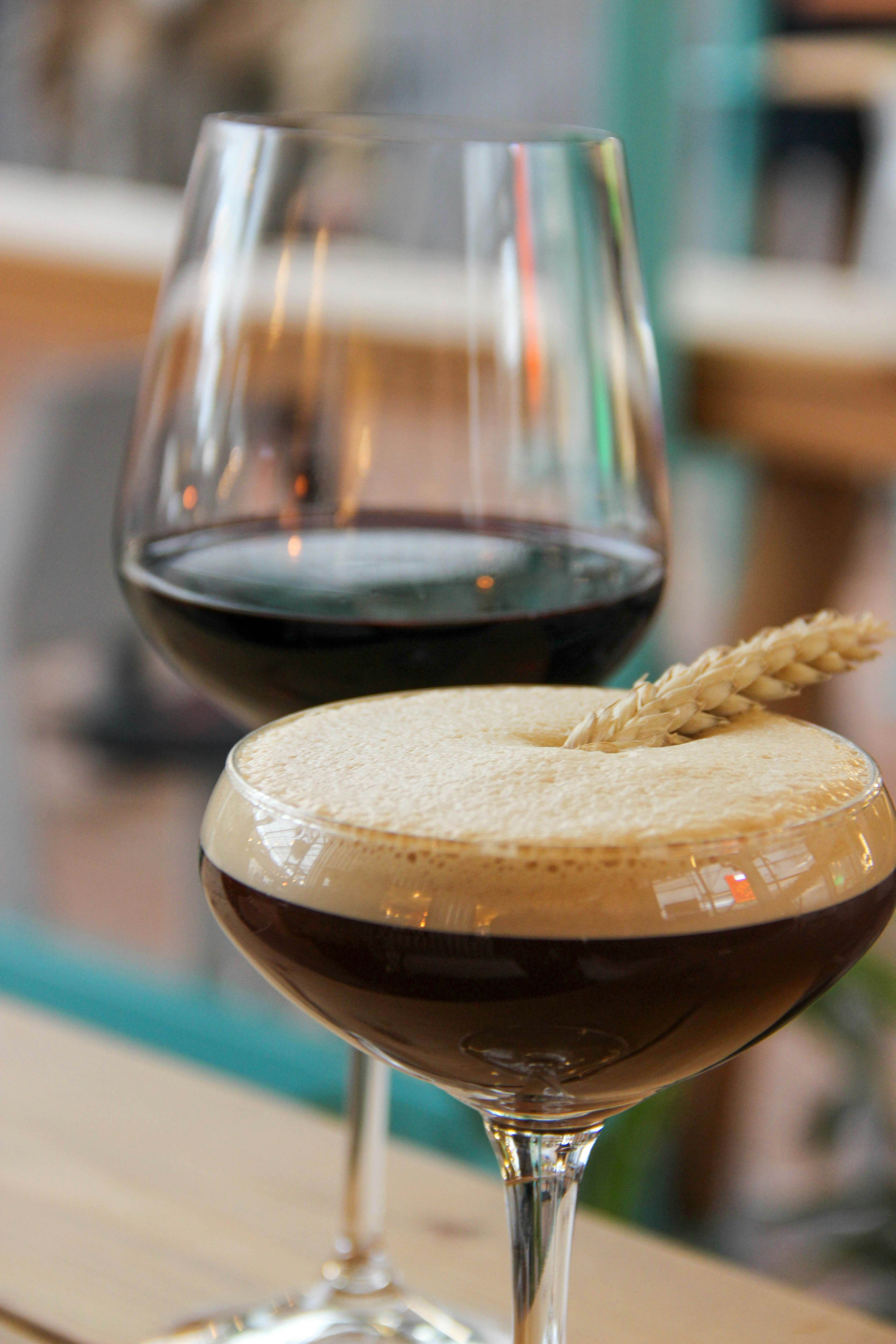 Closely framed shot of a foamy cocktail and a glass of red wine on a wooden table.