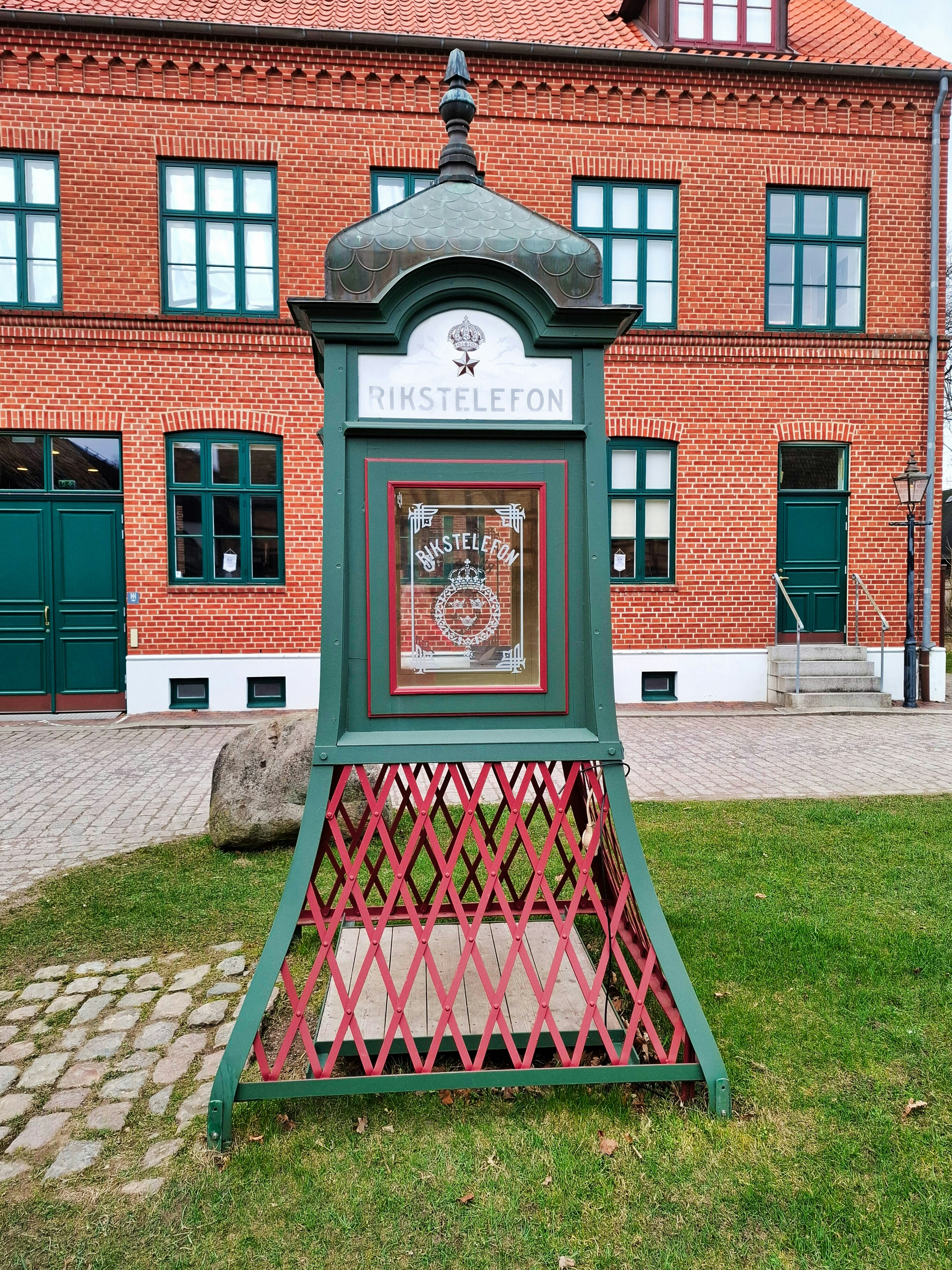 Ornate vintage telephone box set against a historic brick building with green accents.