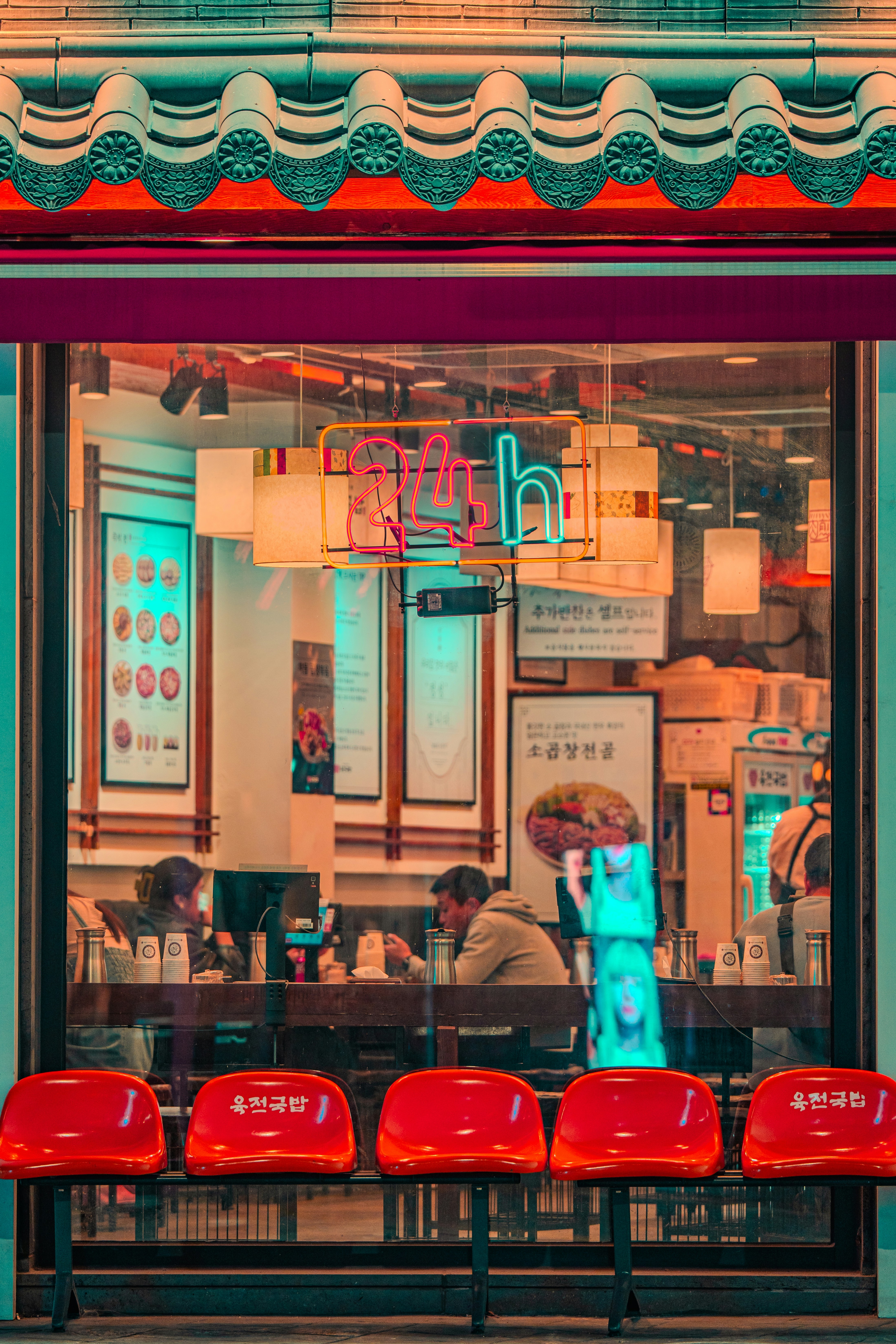 24h Neon Through Glass: A Quiet Diner Framed by Red Seats