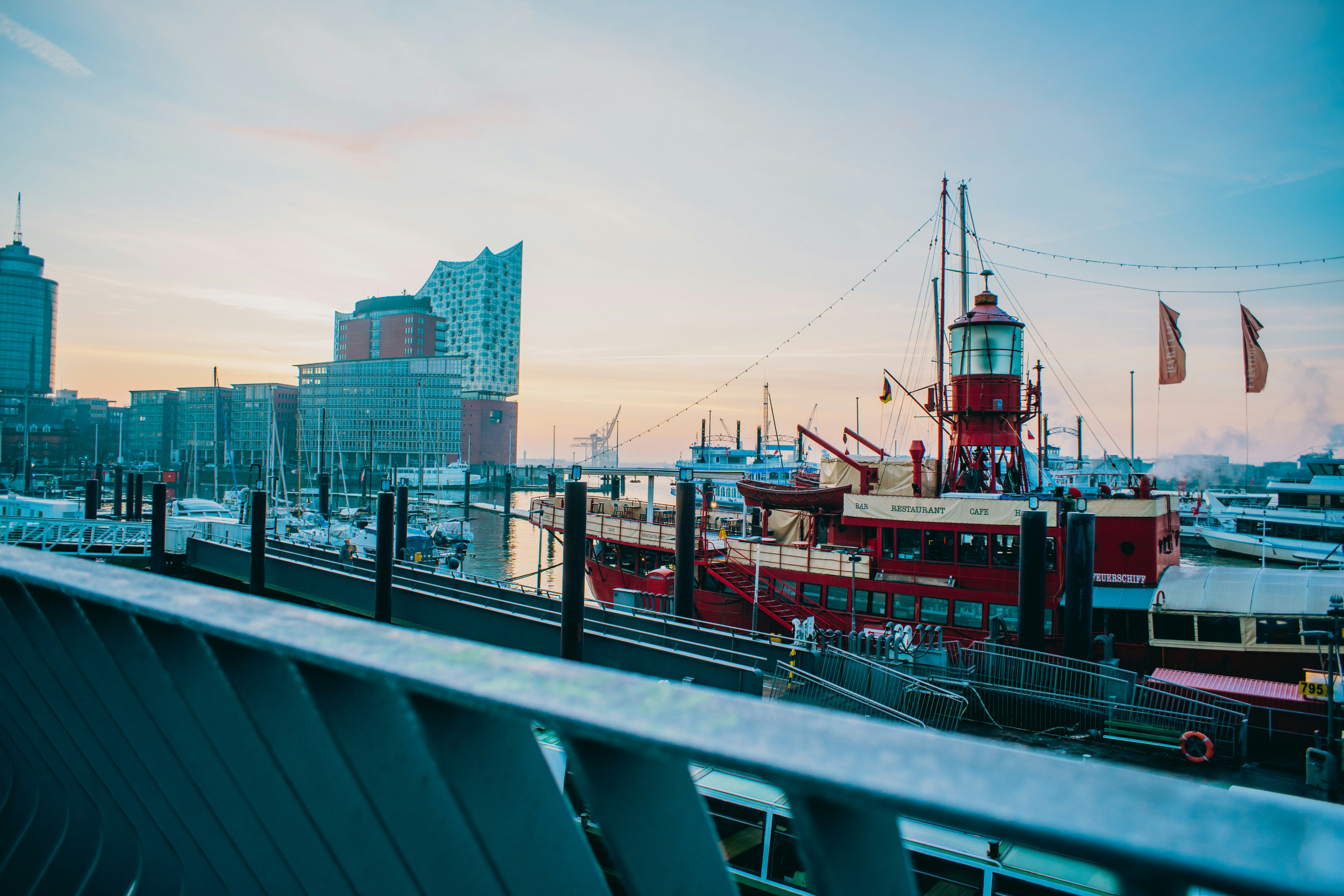 Colorful boats docked in Hamburg's harbor against a pastel sky at dawn.
