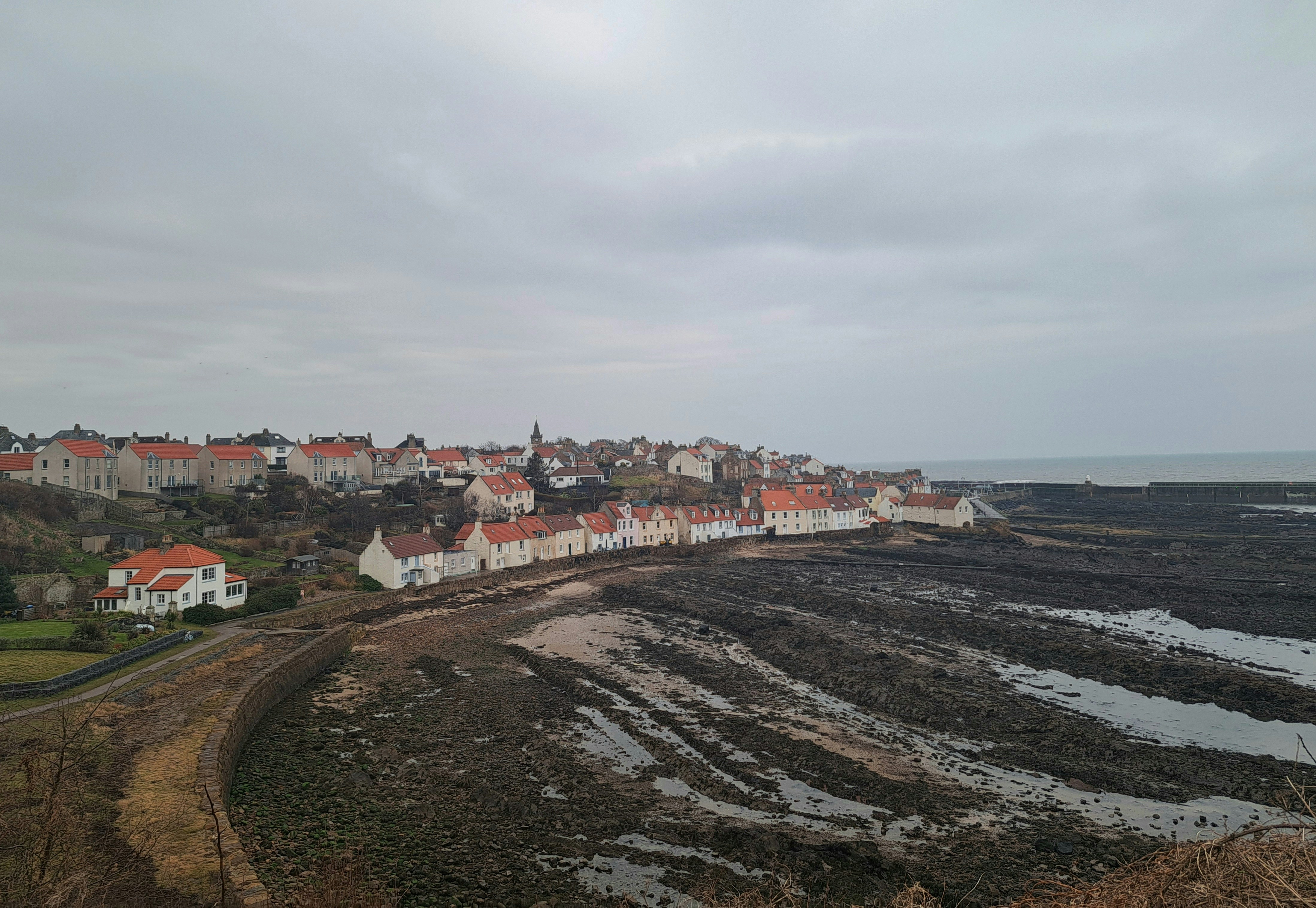 Quaint seaside village with red-roofed houses lining a rocky shoreline under a cloudy sky.