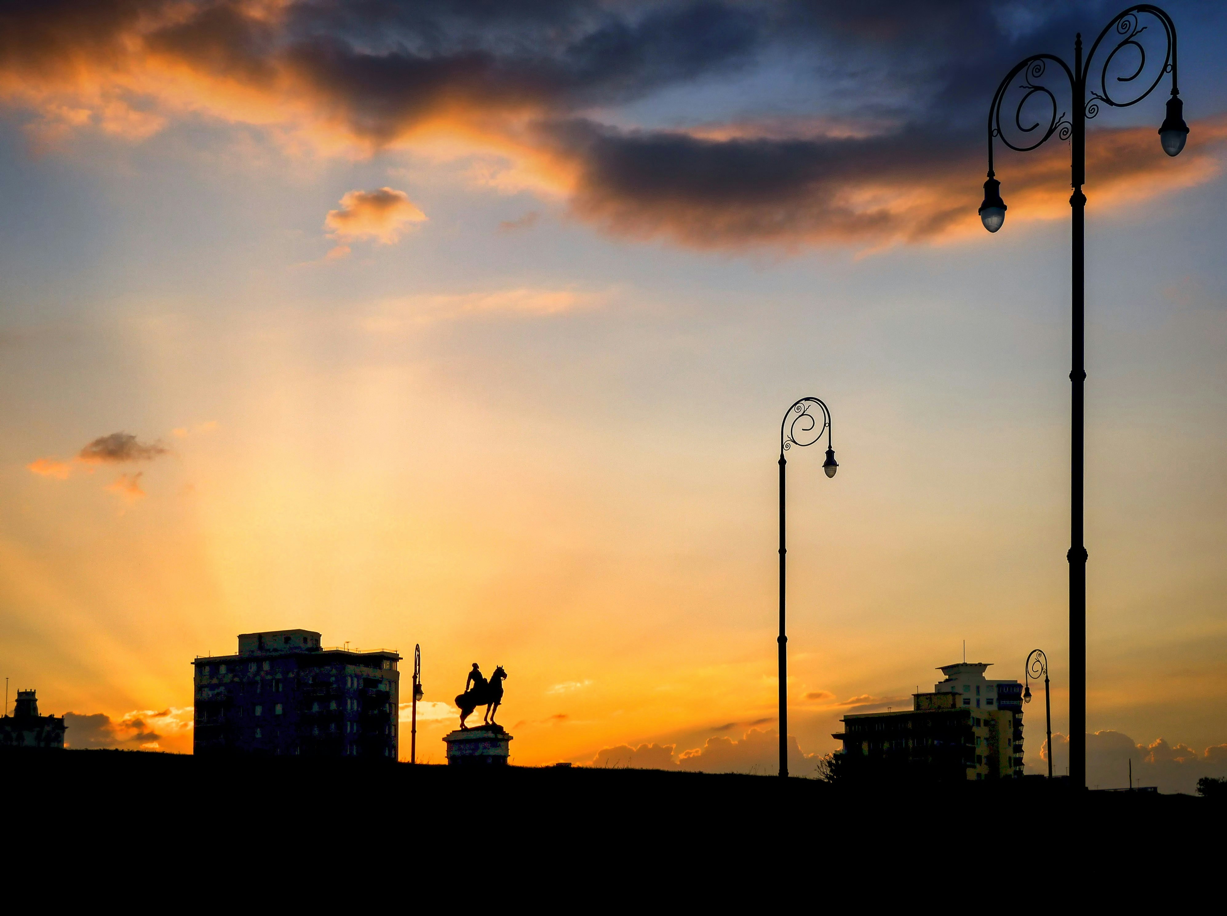 Silhouette of an equestrian statue and street lamps against a vibrant sunset in Havana, Cuba.