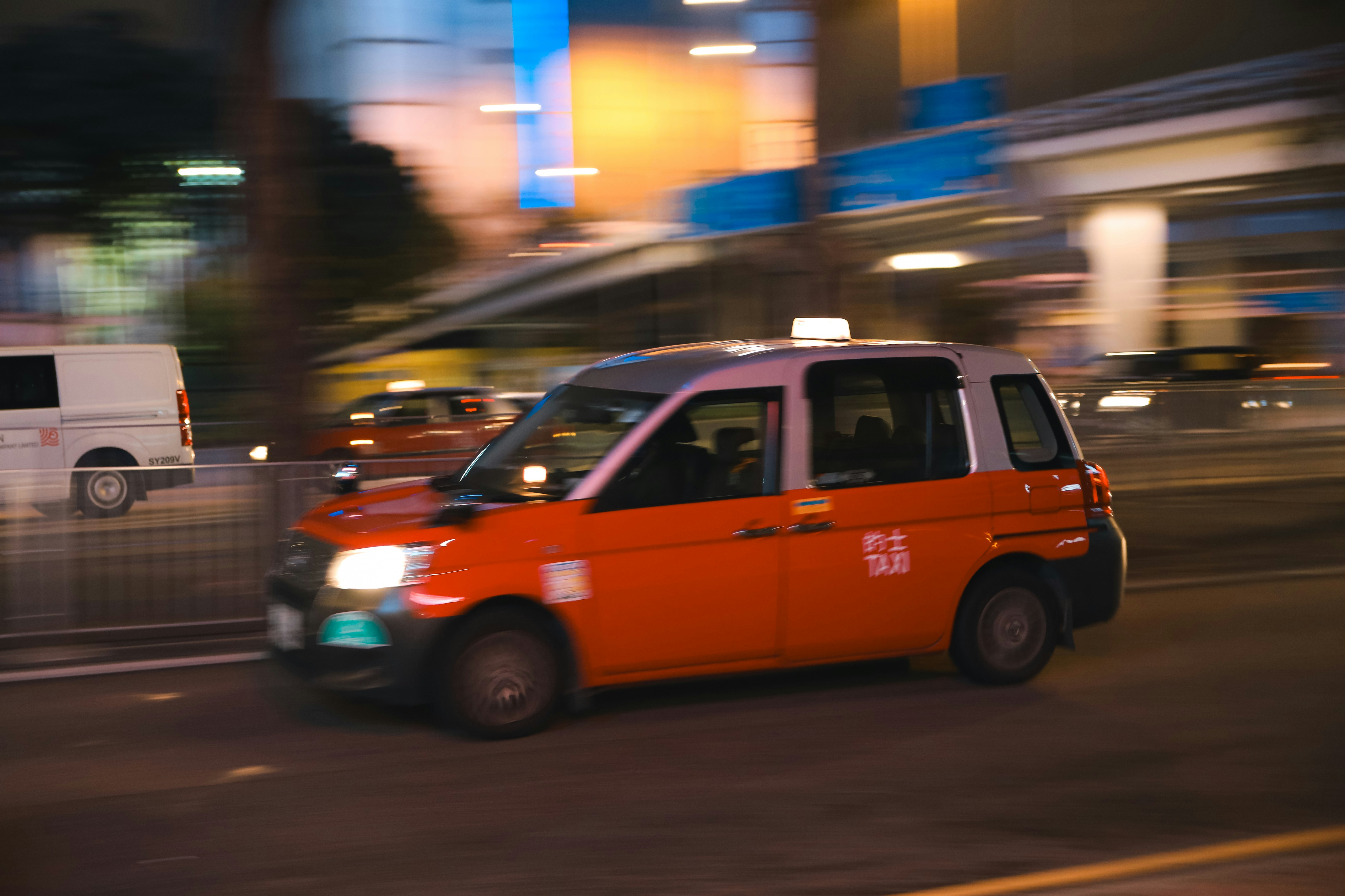 An orange taxi speeds along a city street at night. photo – Free Car ...