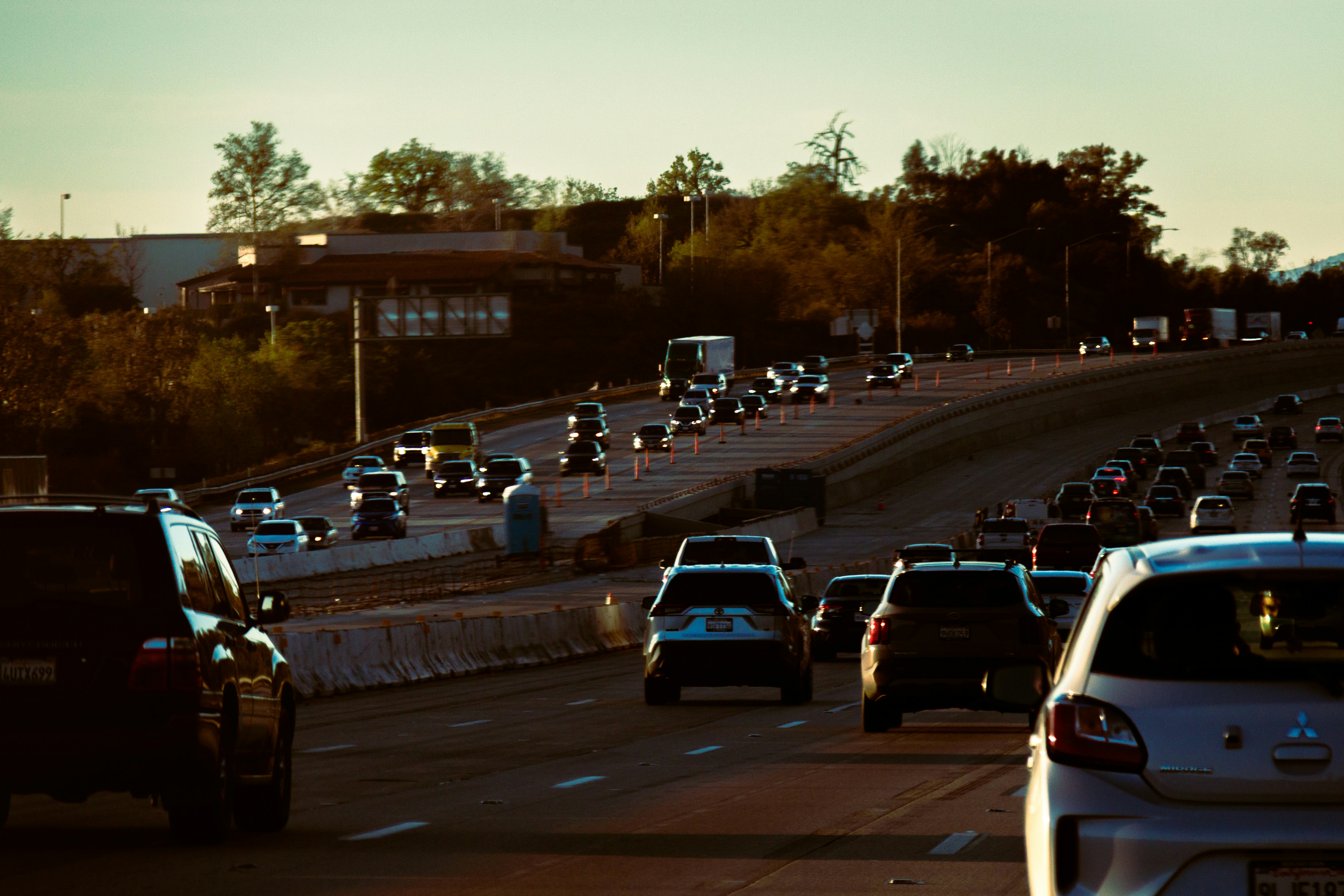 A bustling highway during the evening rush hour, filled with a stream of vehicles and illuminated by the setting sun.