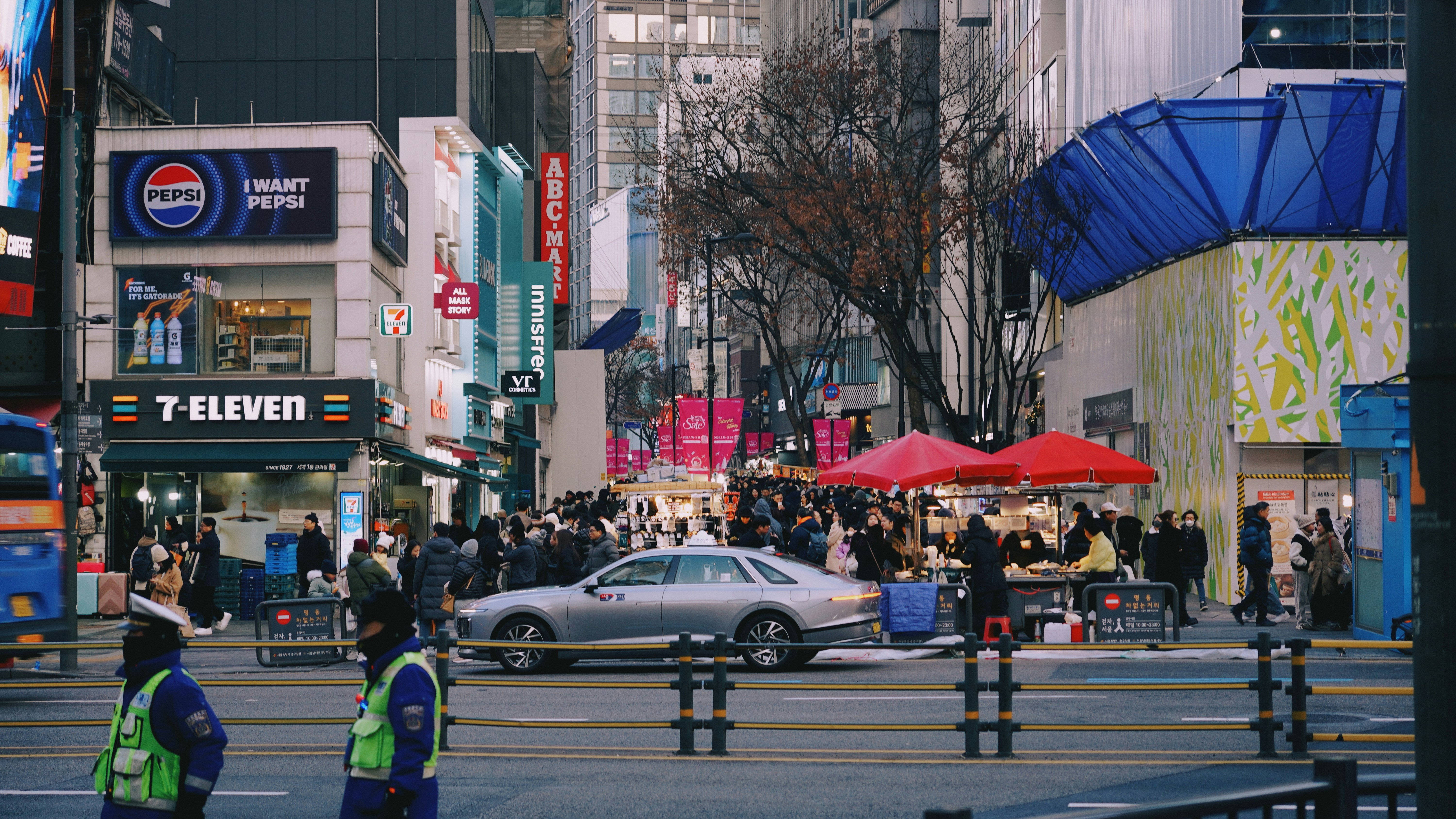Crowded street scene in Myeong-dong, Seoul, with market stalls and pedestrians under vibrant umbrellas.