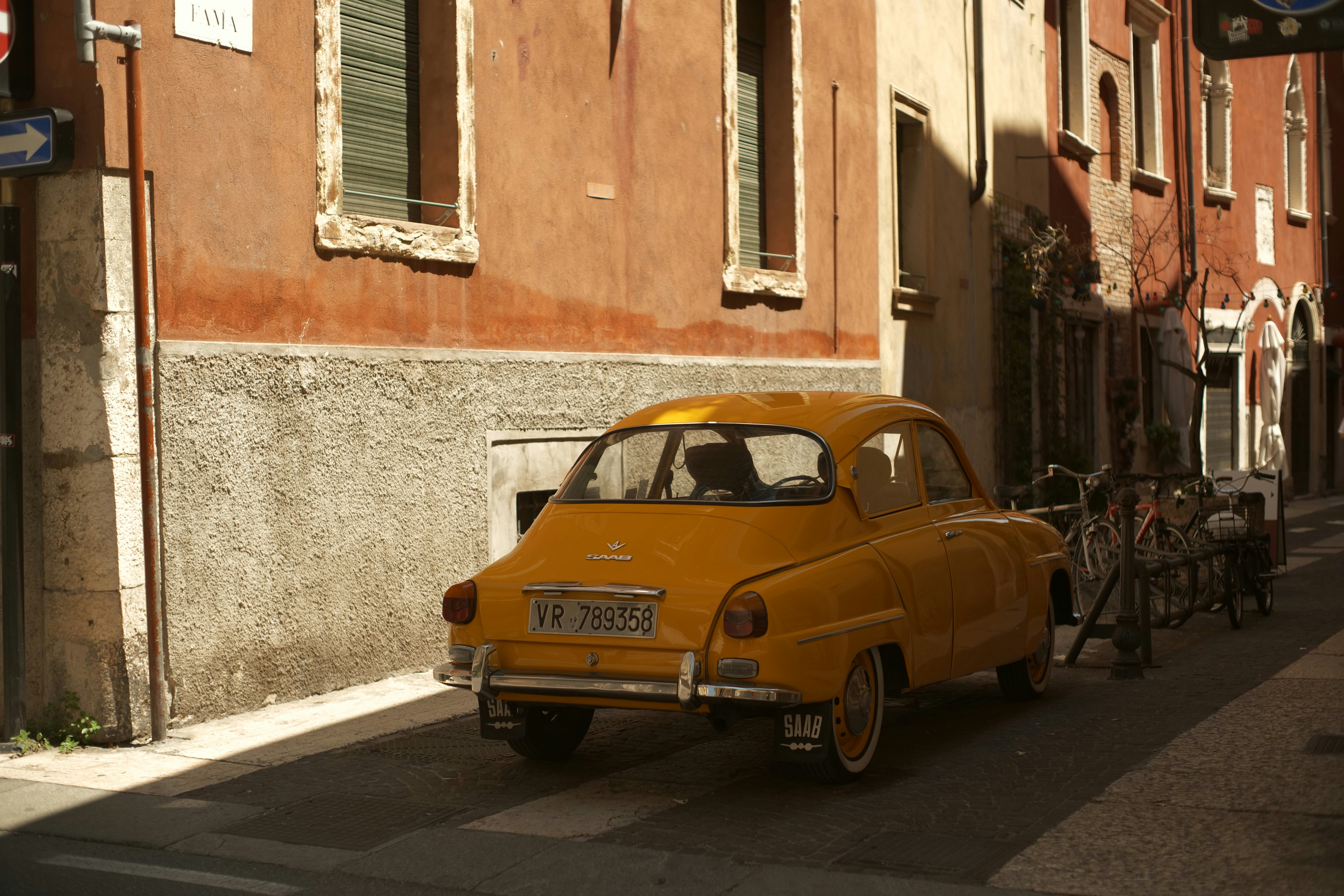 Classic yellow car parked on a narrow street with sunlight casting shadows from the buildings.