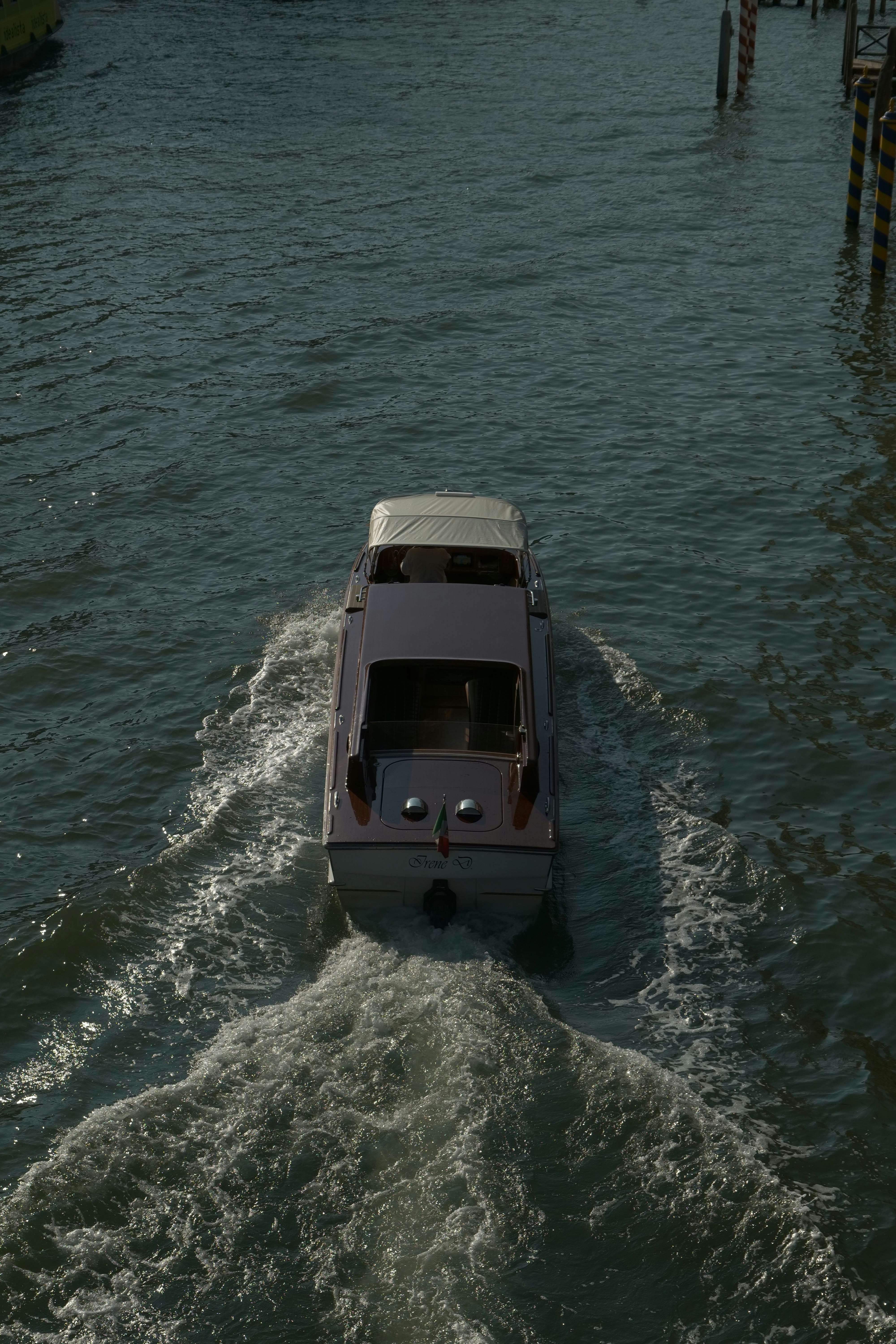 Motorboat creating ripples on a wide river under soft sunlight.