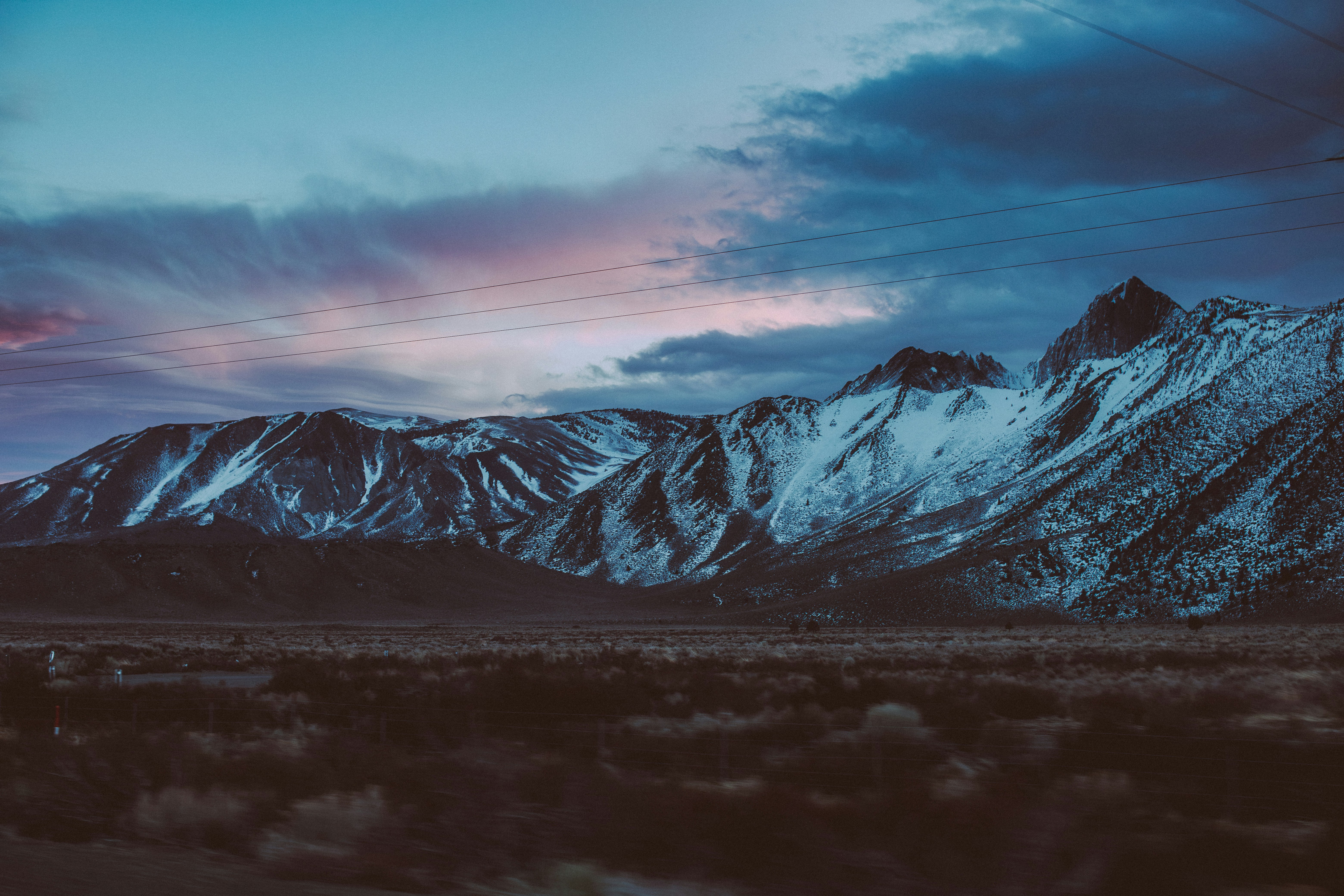 Snow-covered mountains under a vibrant twilight sky with hues of purple and blue.