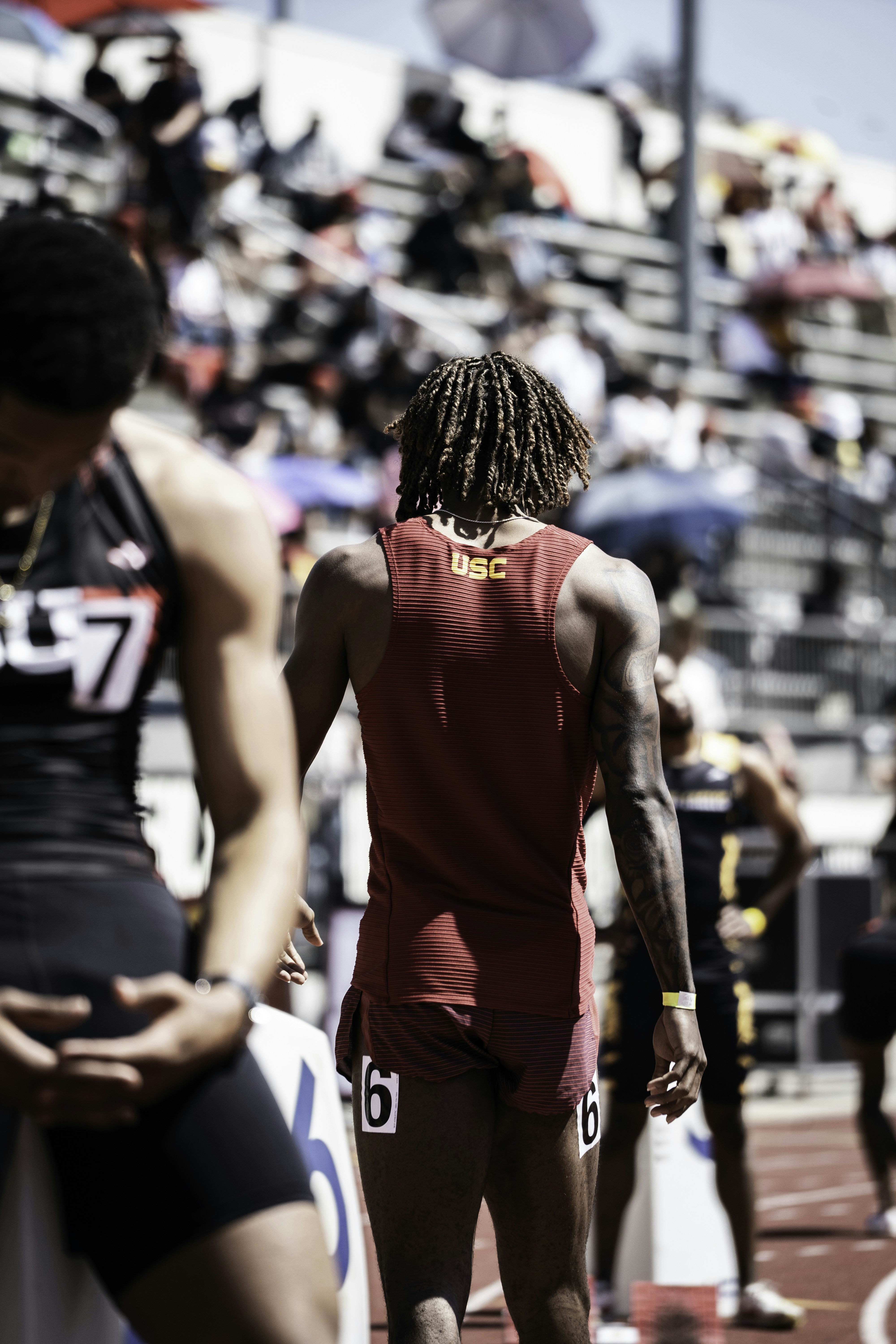 Athletes stand poised at the starting line of an outdoor track event under bright sunlight.