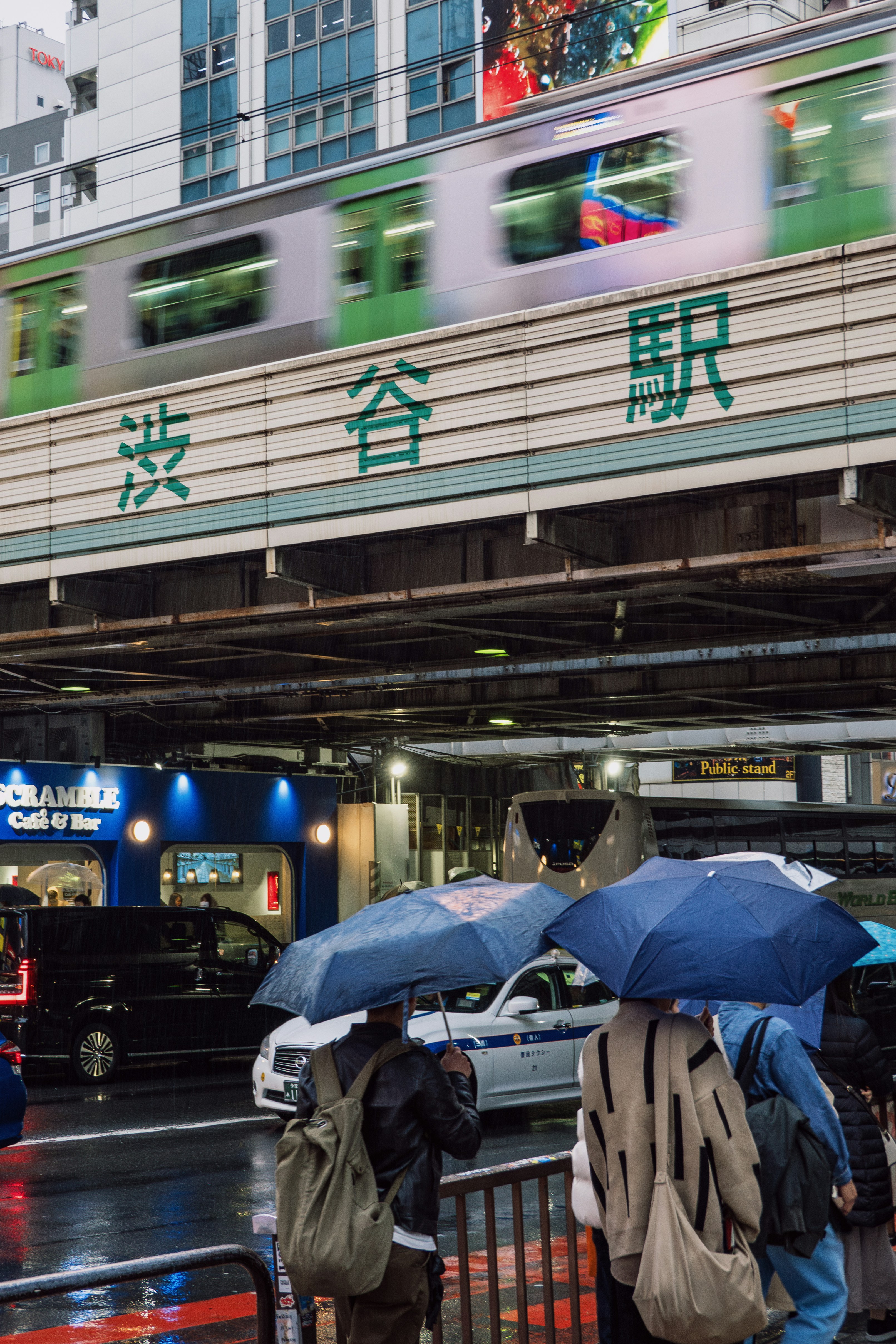 People with umbrellas wait under a train in shibuya. photo – Free Car ...