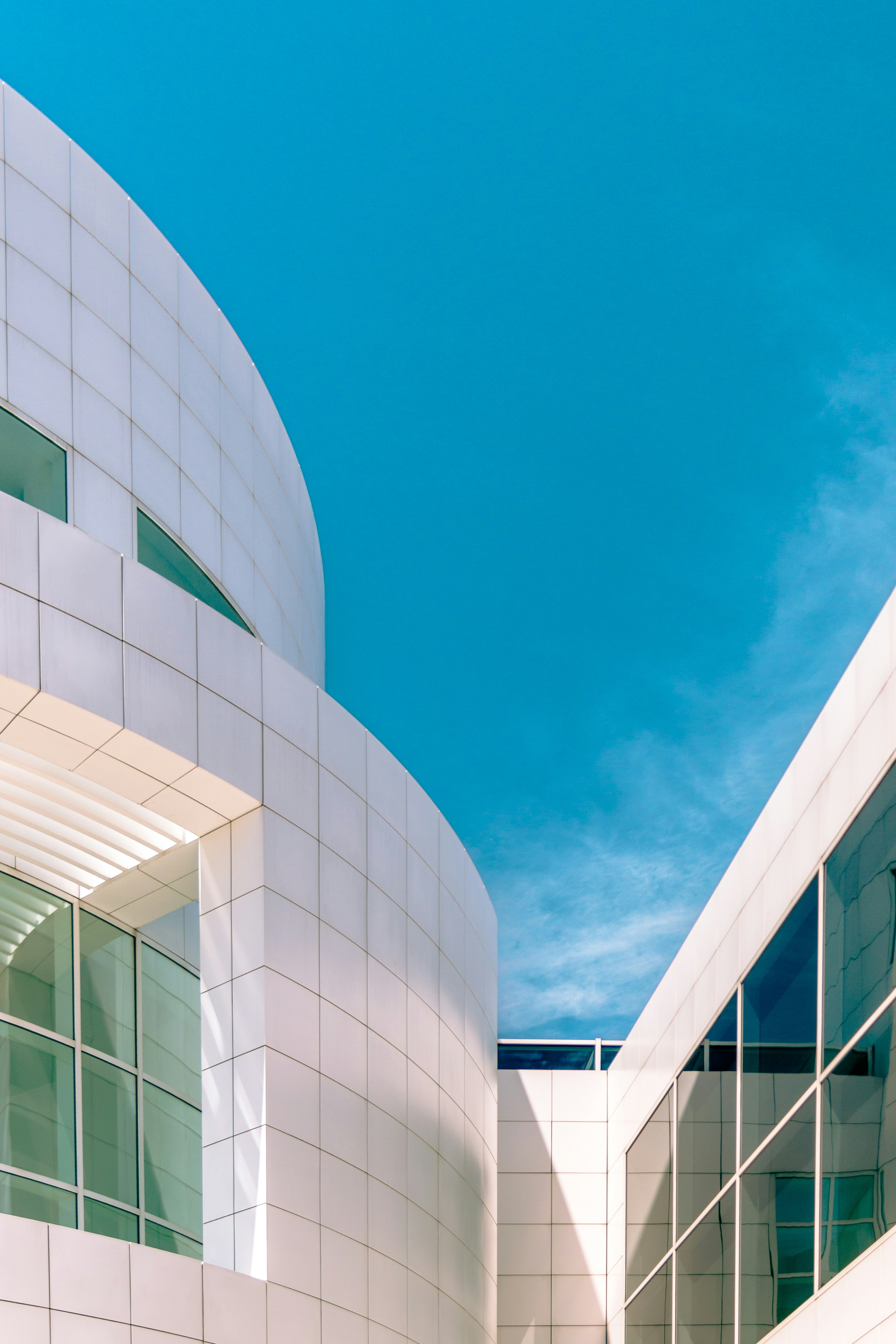 Curved modern building with white panels and glass windows under a clear blue sky.