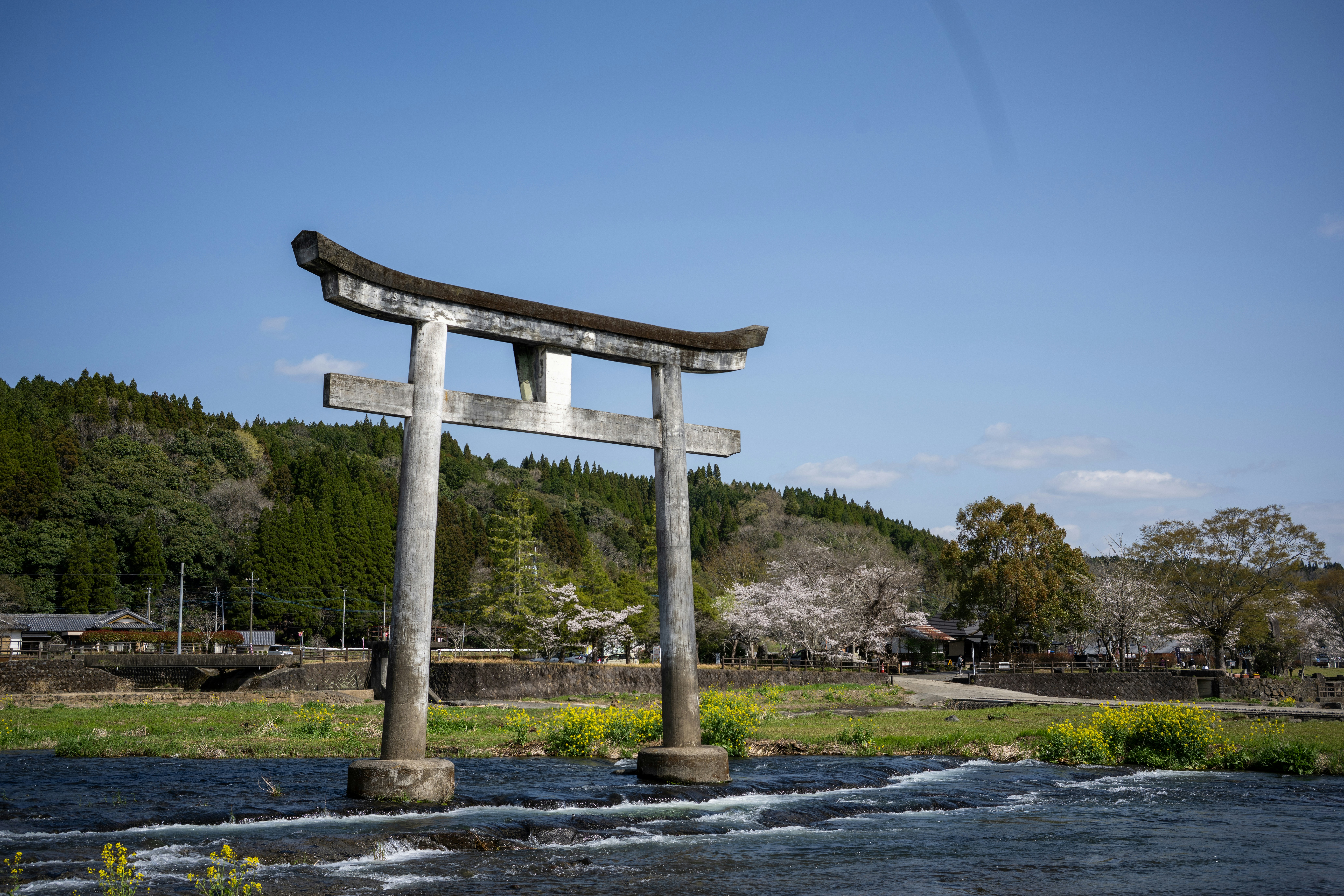 Torii gate standing in river with lush green hills and blue sky.