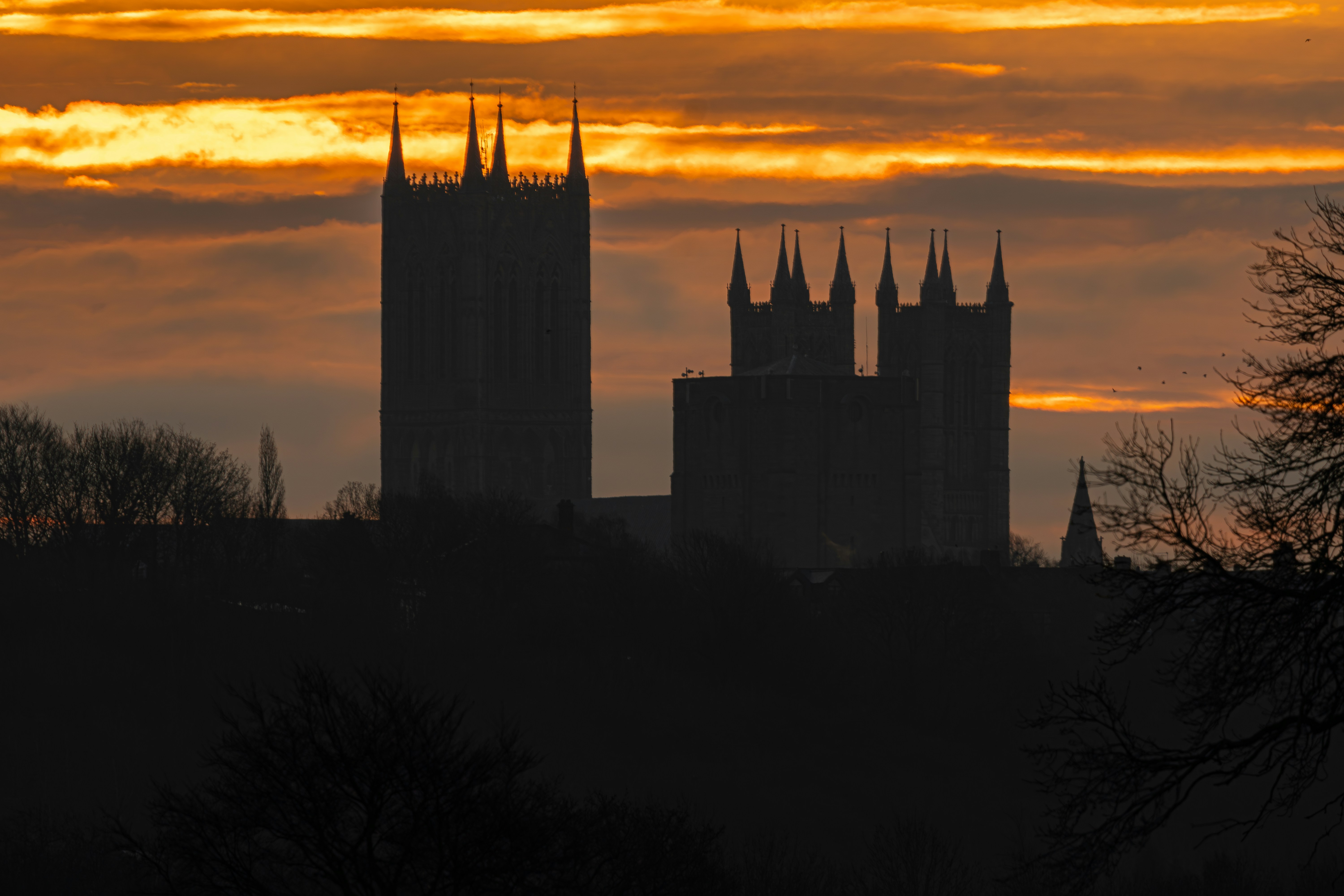 Silhouette of a cathedral with multiple spires set against a vibrant orange sunset sky.