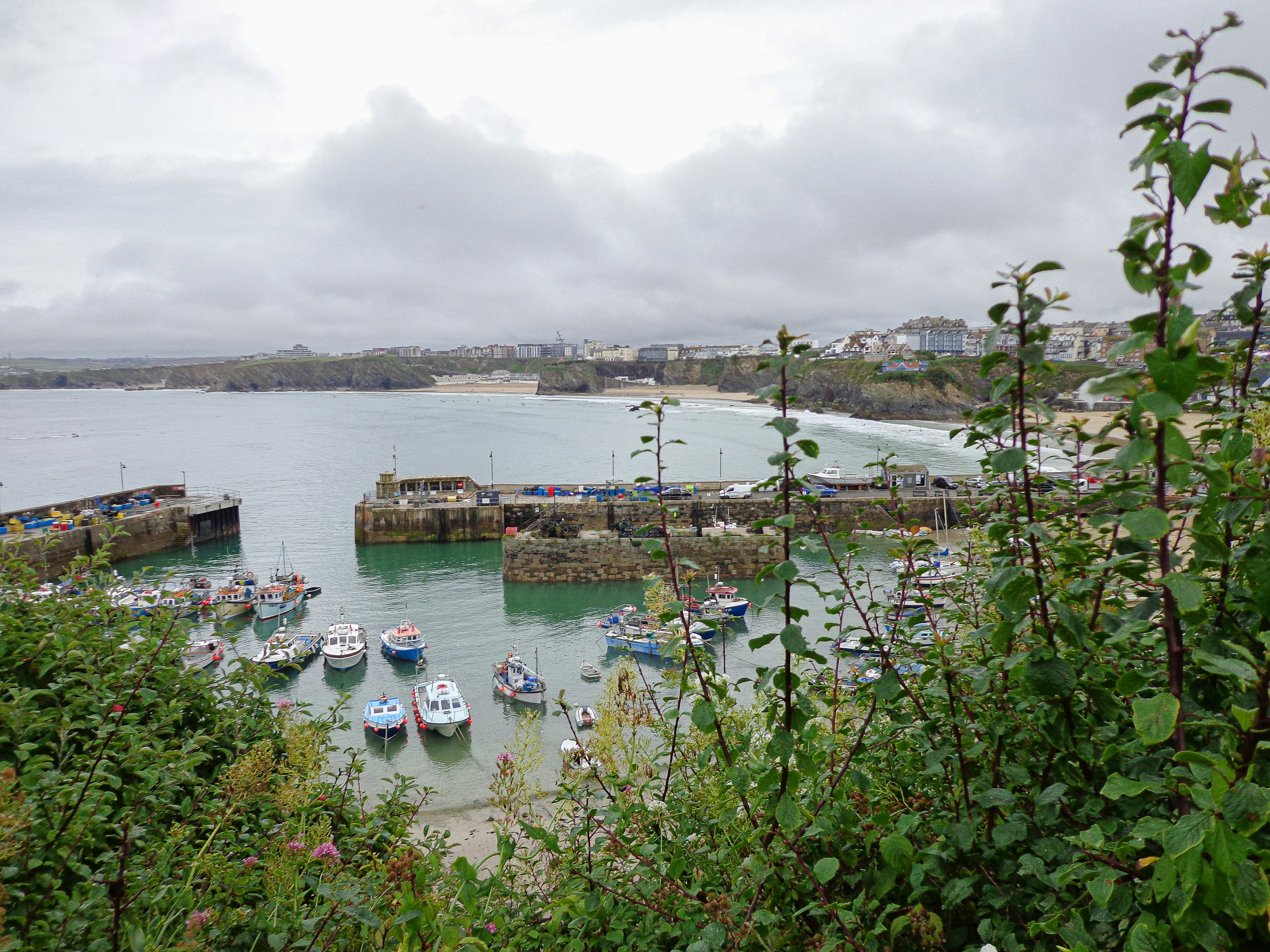 Small boats docked in a tranquil harbor surrounded by lush greenery under a cloudy sky.