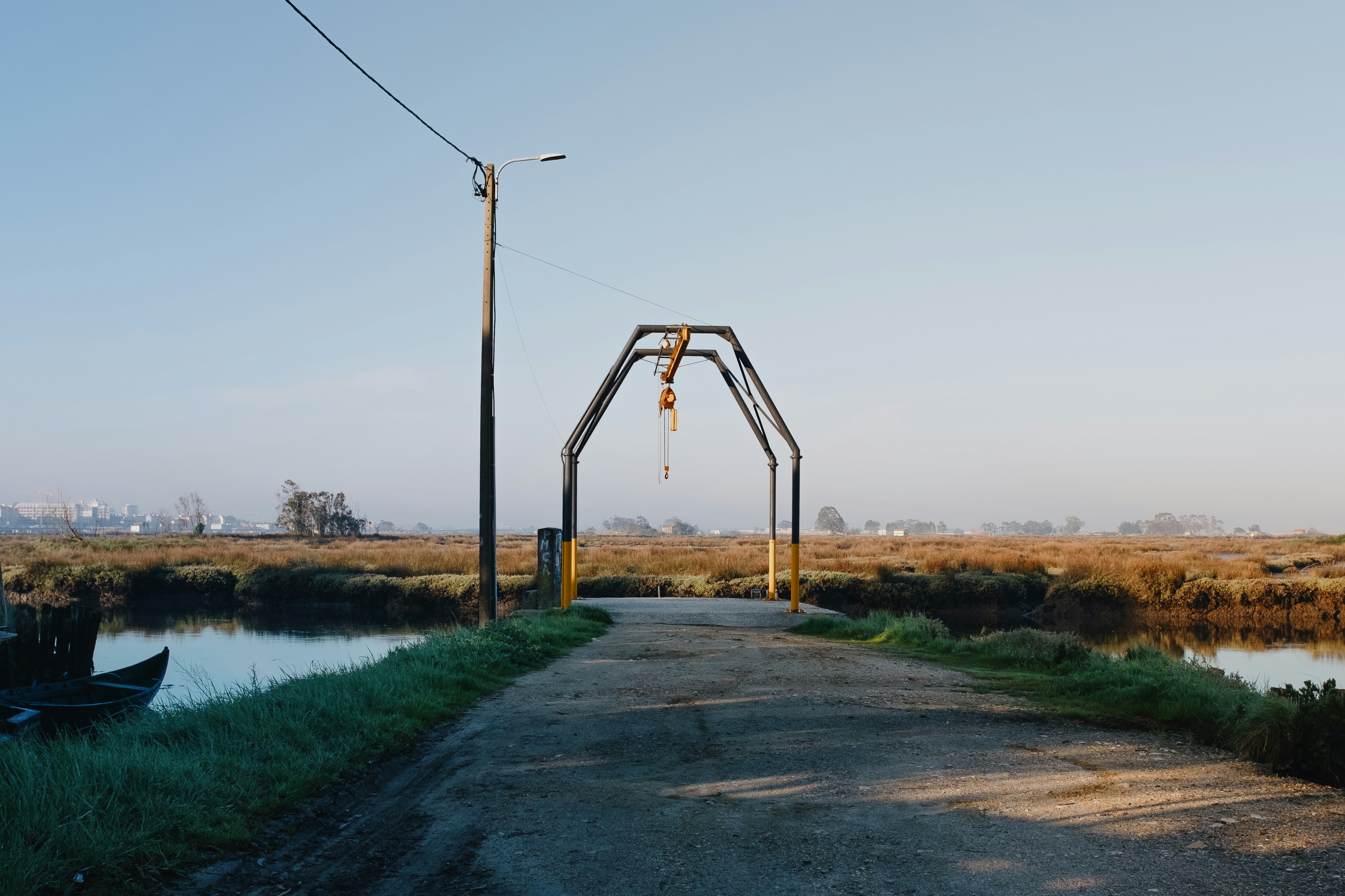 Rural road leading to a metal structure over a calm waterway under a clear sky.