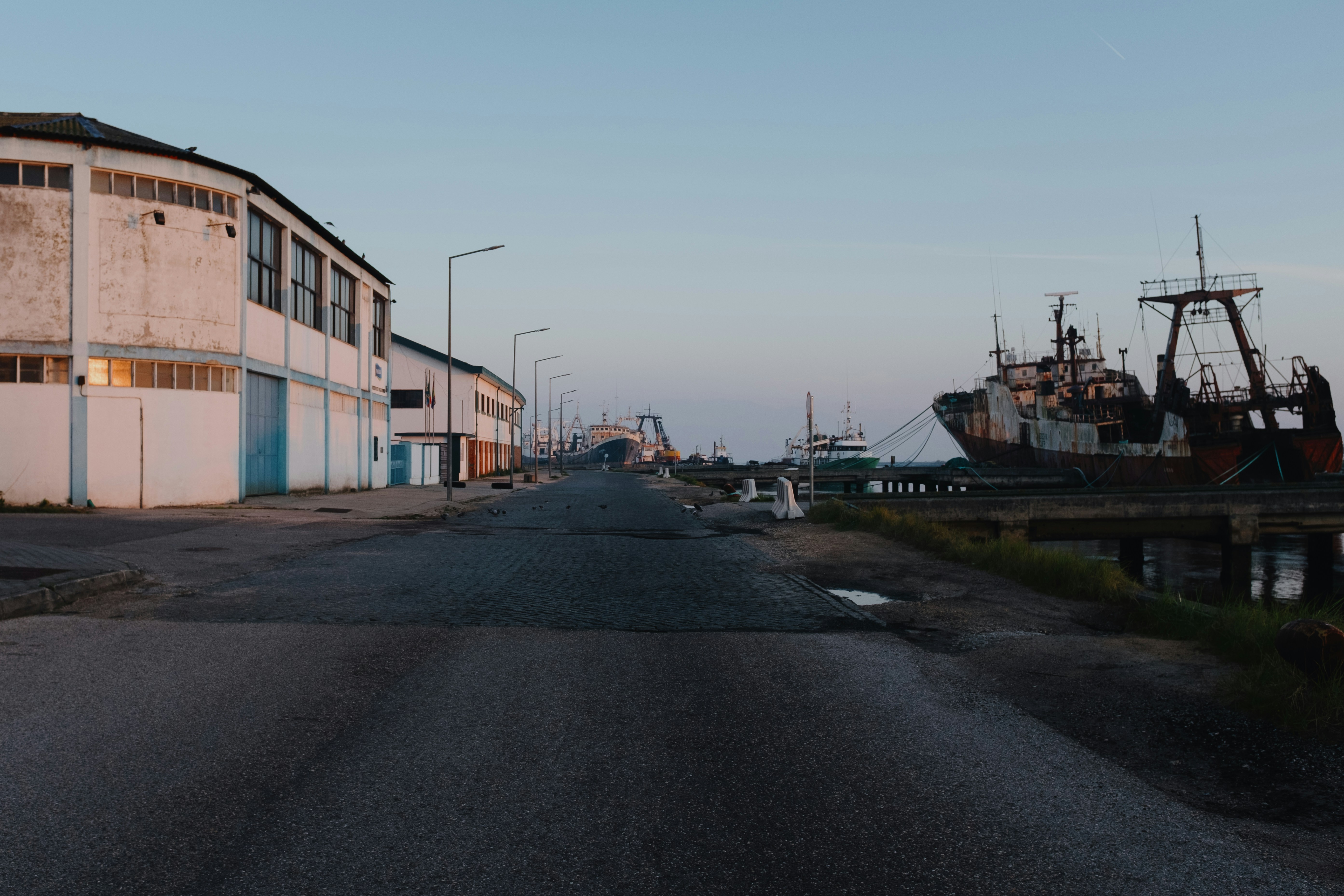 Deserted industrial waterfront with a moored fishing vessel under a clear evening sky.