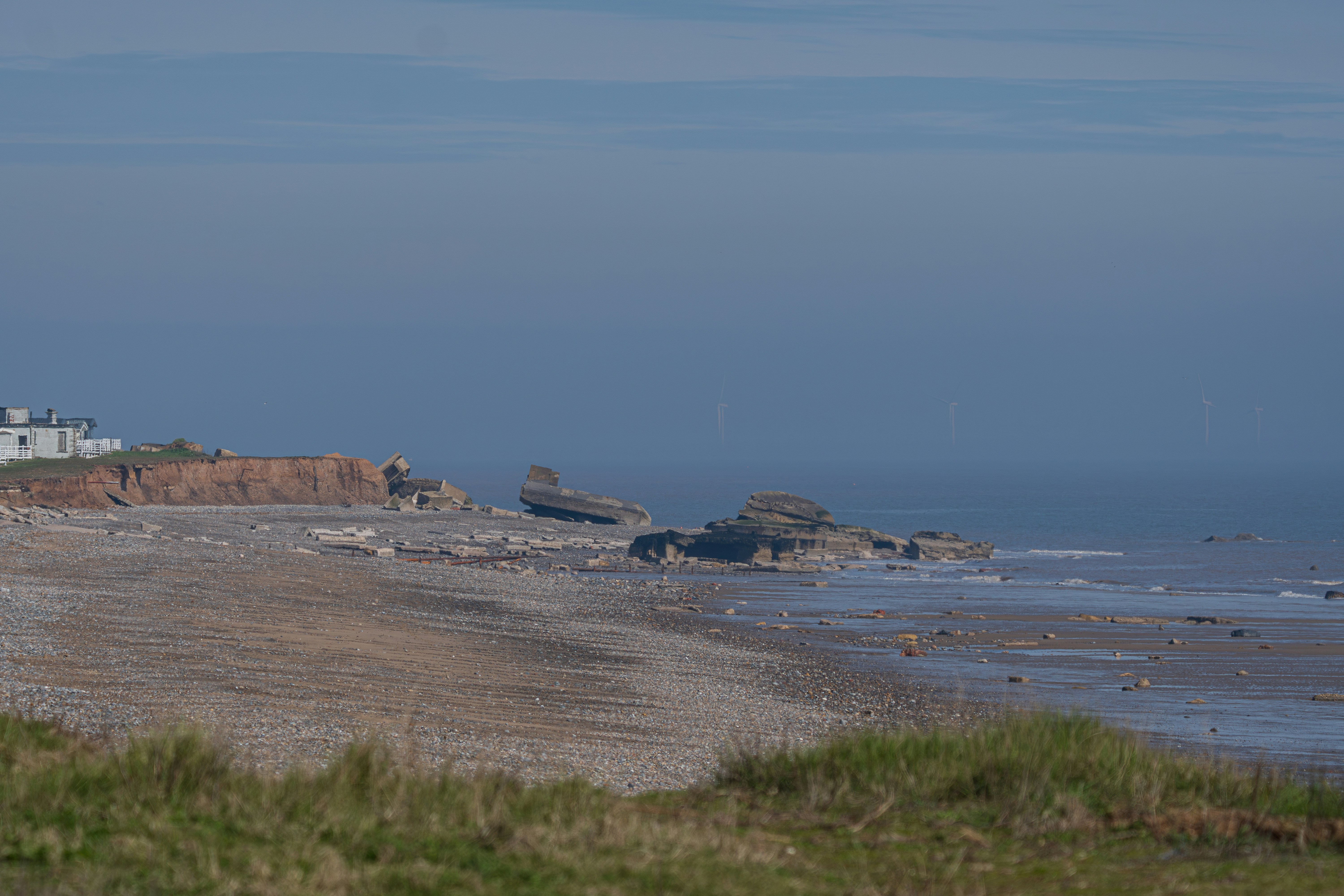 Waves gently lap against a sandy beach with distant cliffs under a blue sky.