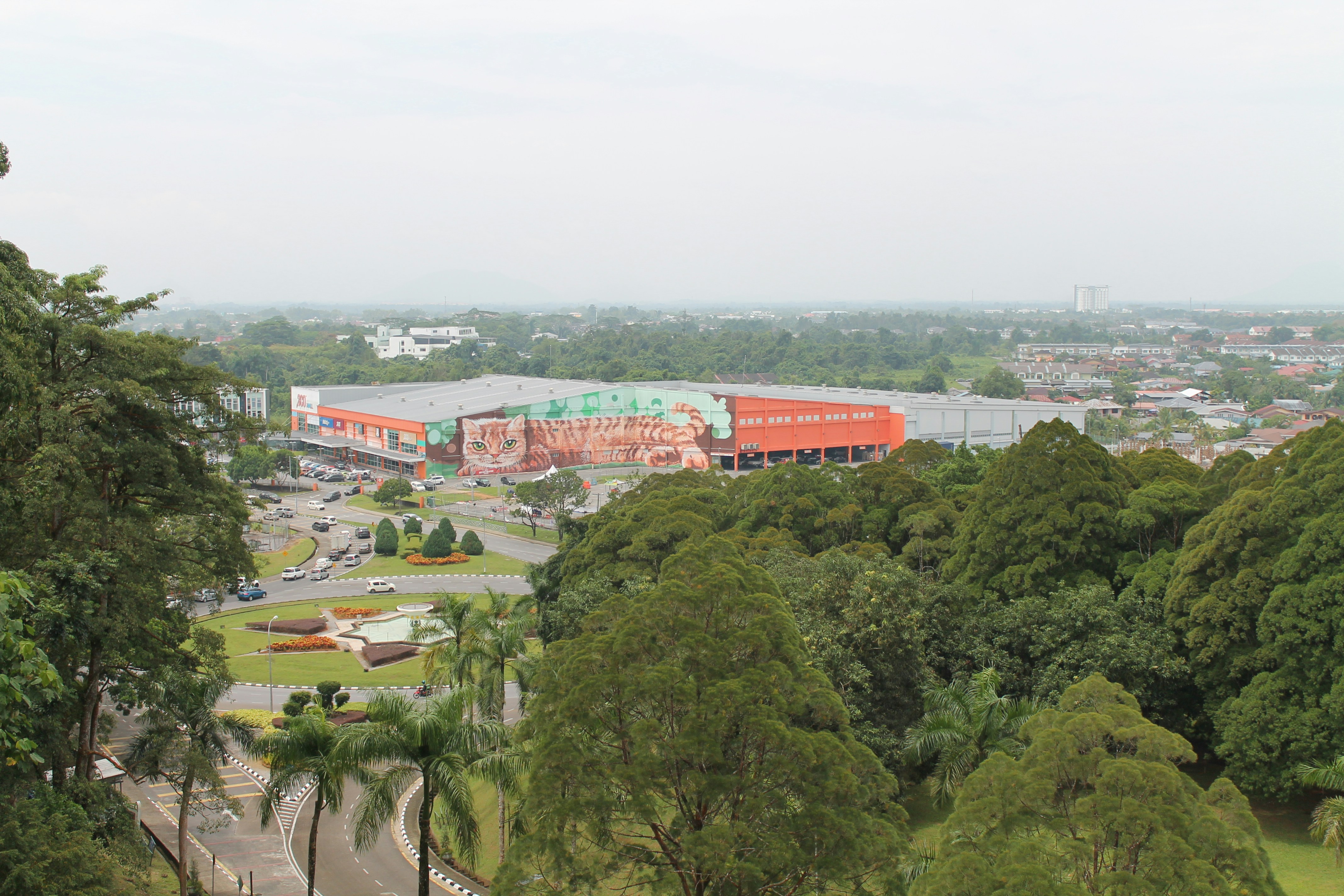 Expansive cityscape with a prominent red building surrounded by lush greenery under an overcast sky.