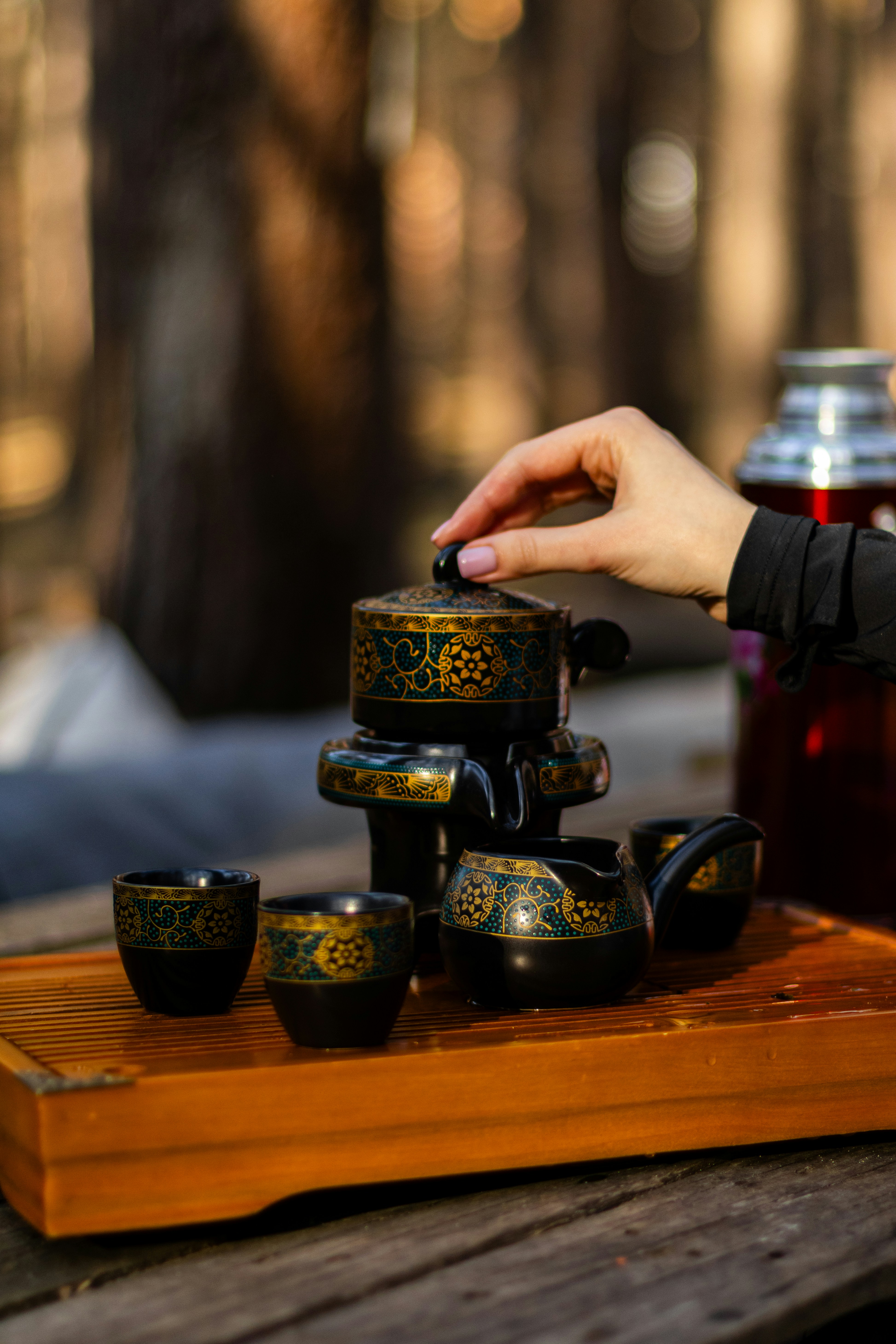 A Quiet Ritual: Hand Adjusts an Ornate Black-and-Gold Tea Set