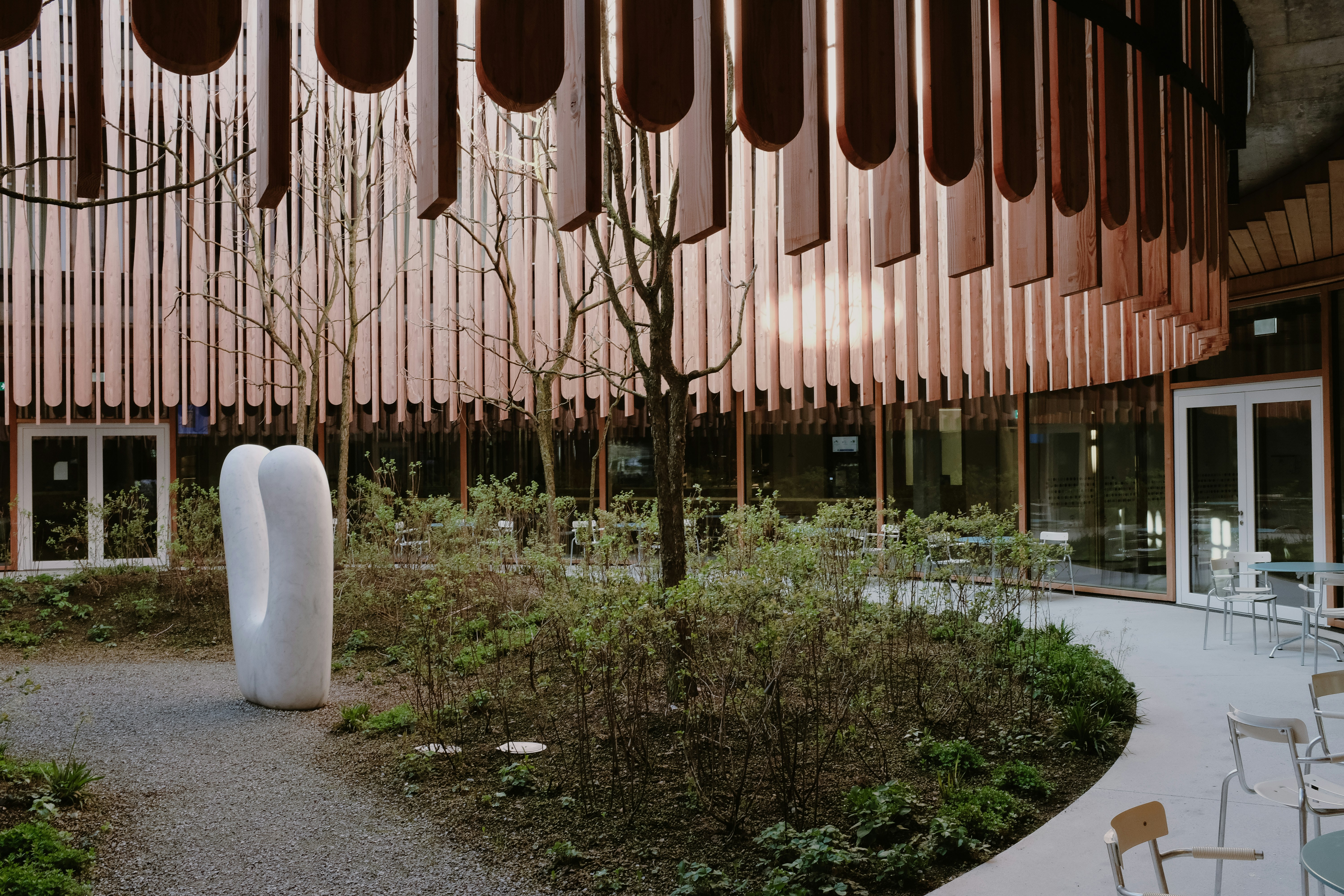 Circular garden with minimalist sculptures and a canopy of vertical wooden slats.