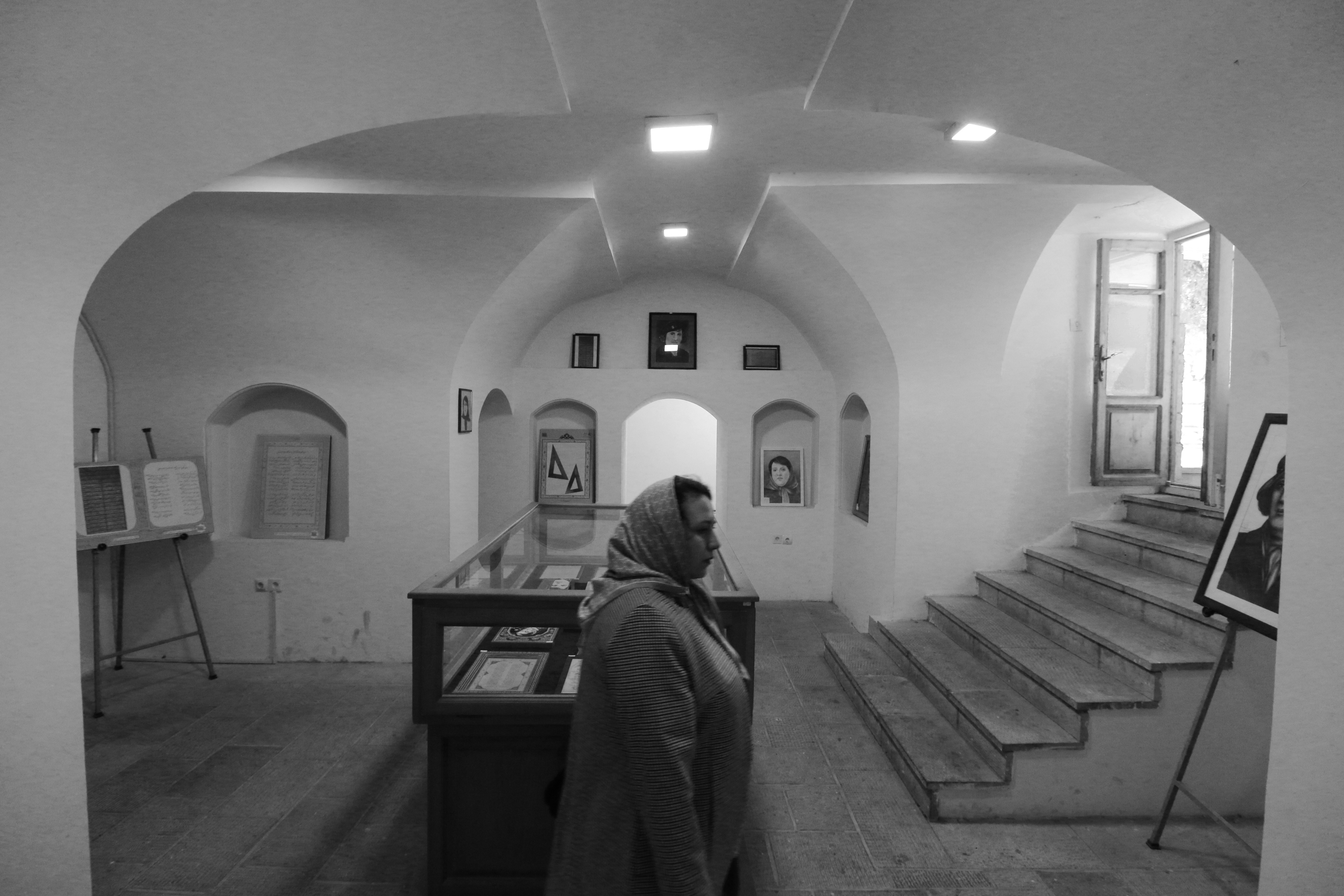 Monochrome view of a person in a historic interior with arched ceilings and framed artwork on the walls.