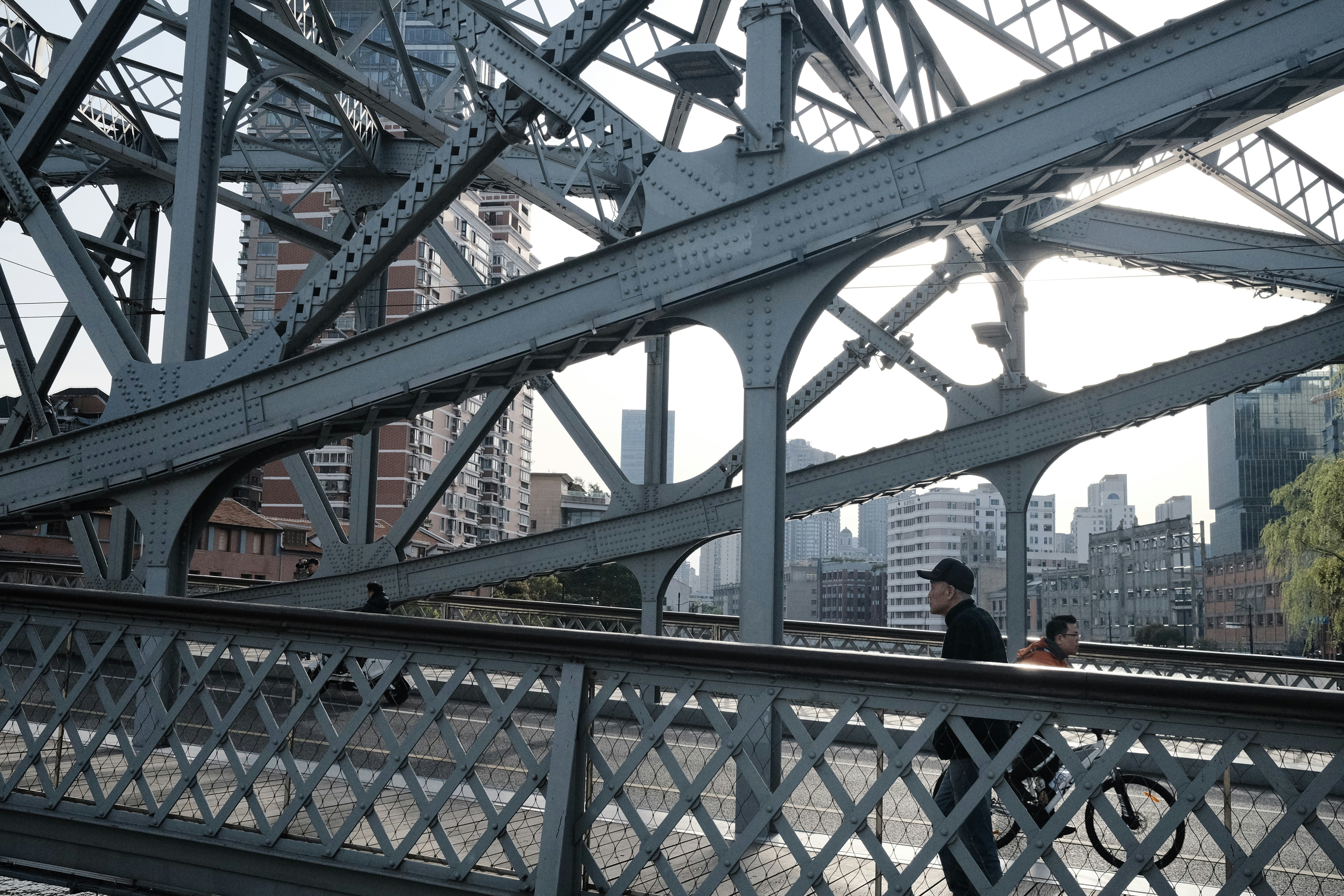Cyclists navigating a steel bridge with a city skyline in the background.