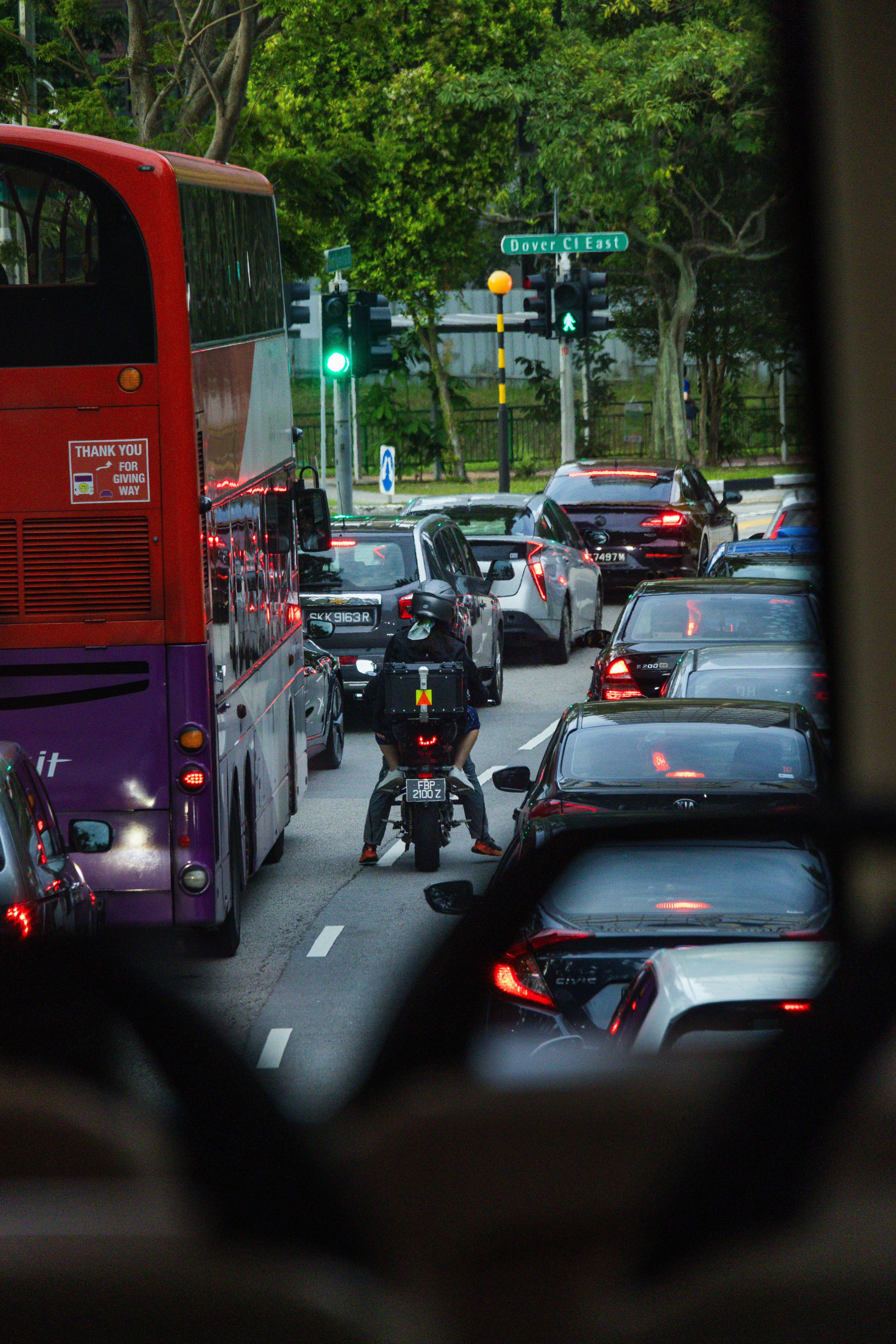 Threading the City Corridor: A Motorcycle Weaves Through a Sea of Cars Past a Red Bus