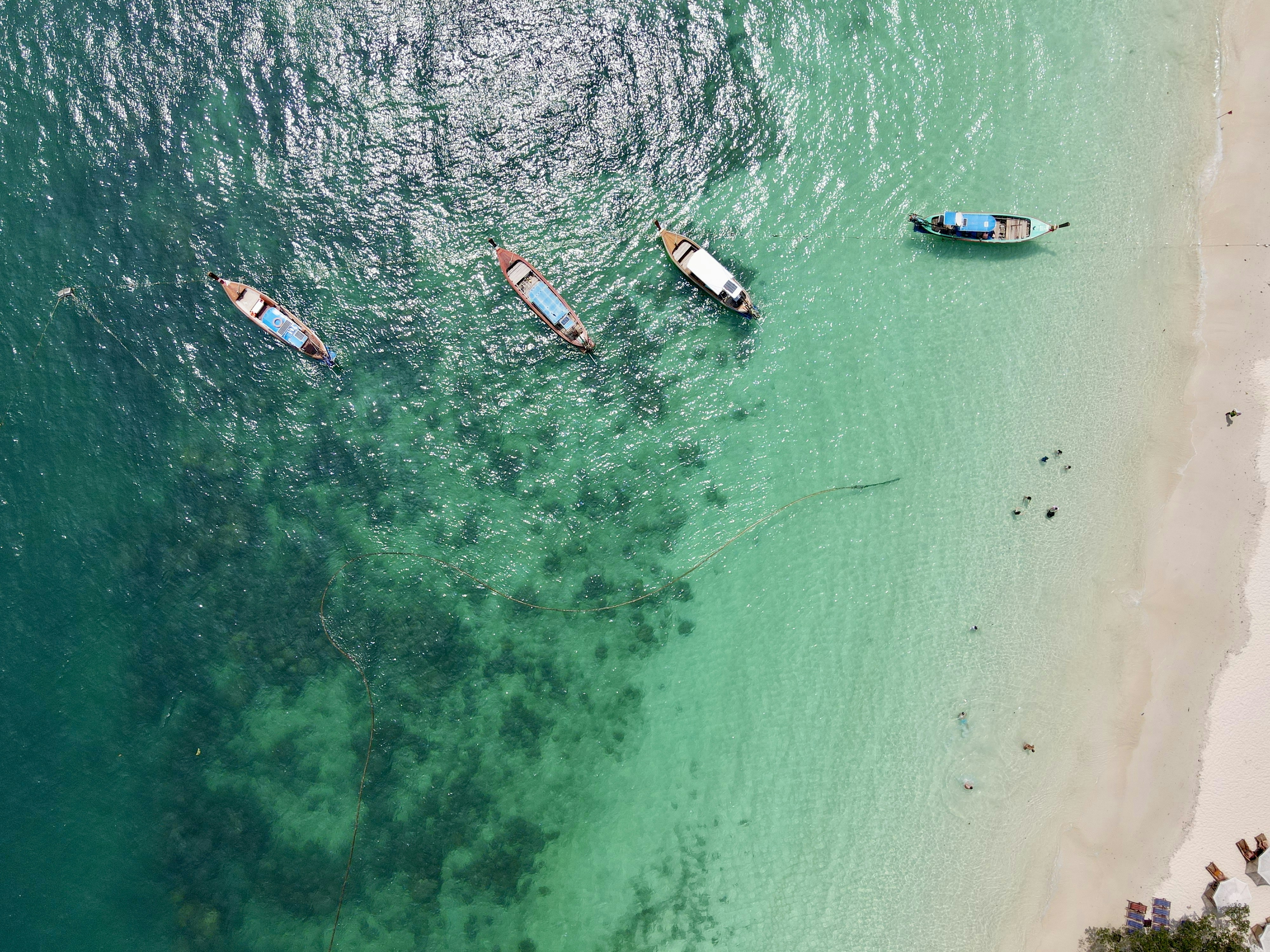 Five boats drift over turquoise waters near a sandy shoreline.