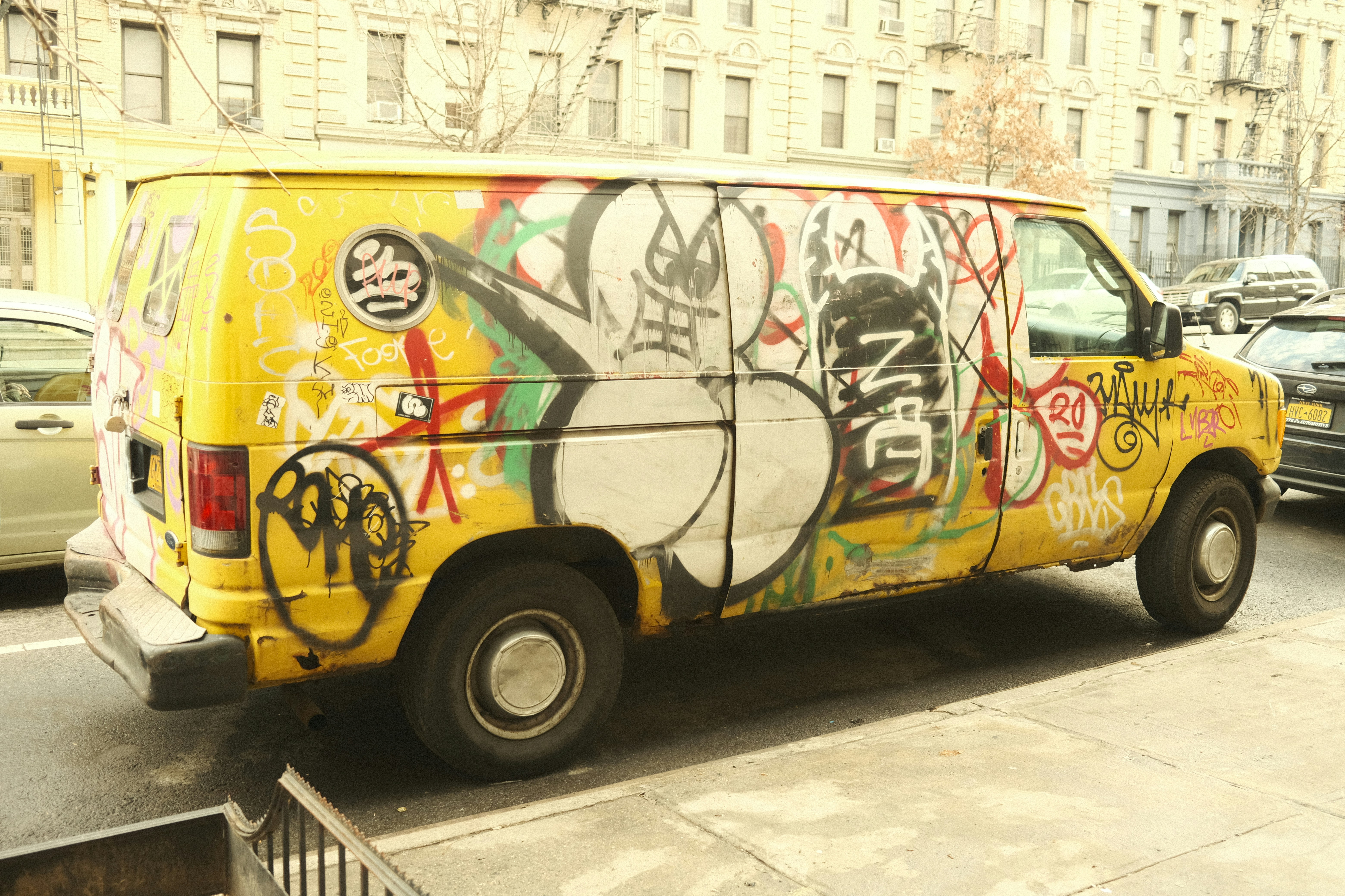 Yellow van adorned with vibrant graffiti parked on a city street.