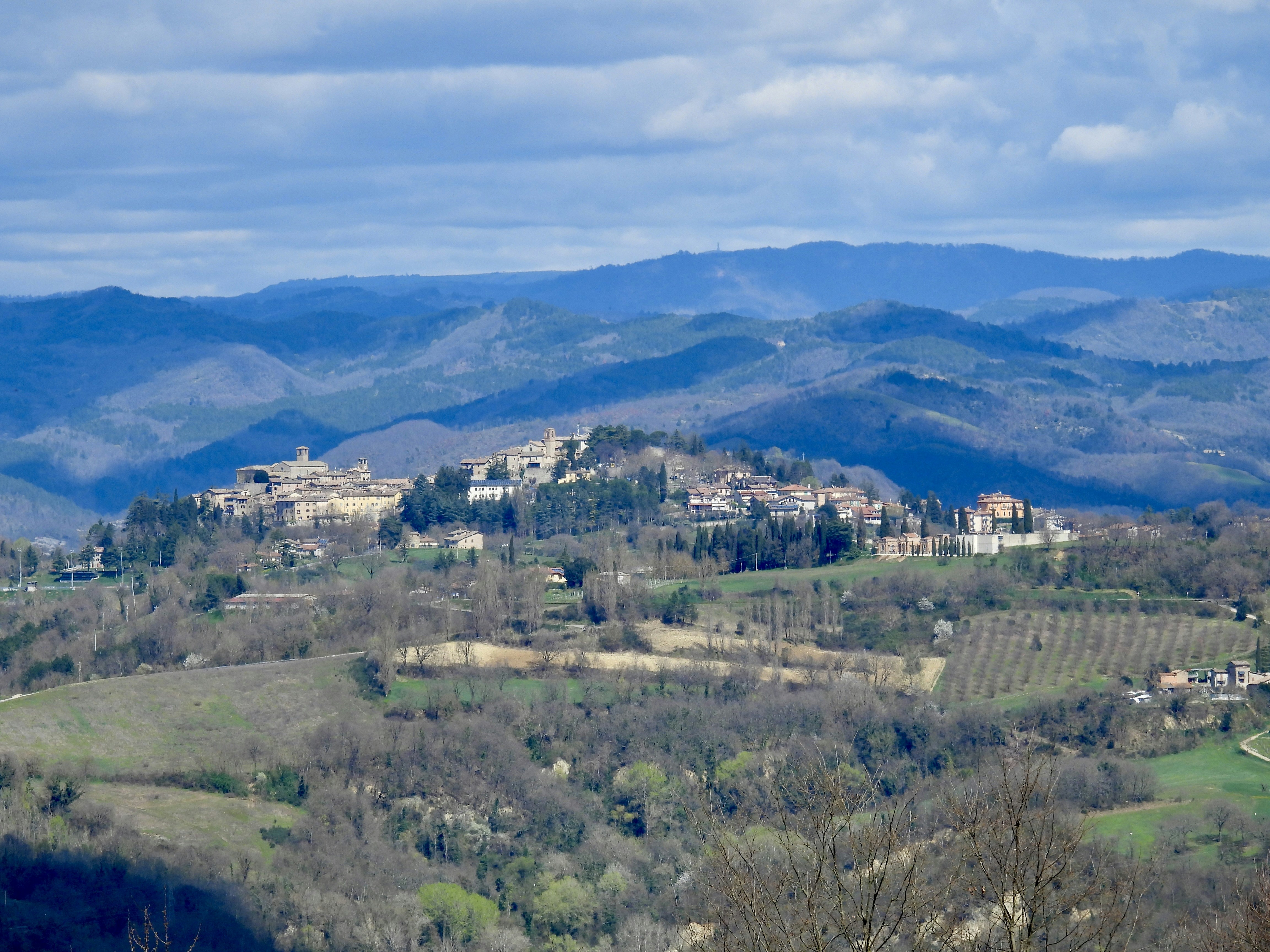 Montone village nestled among verdant hills under a wide, cloud-streaked sky.
