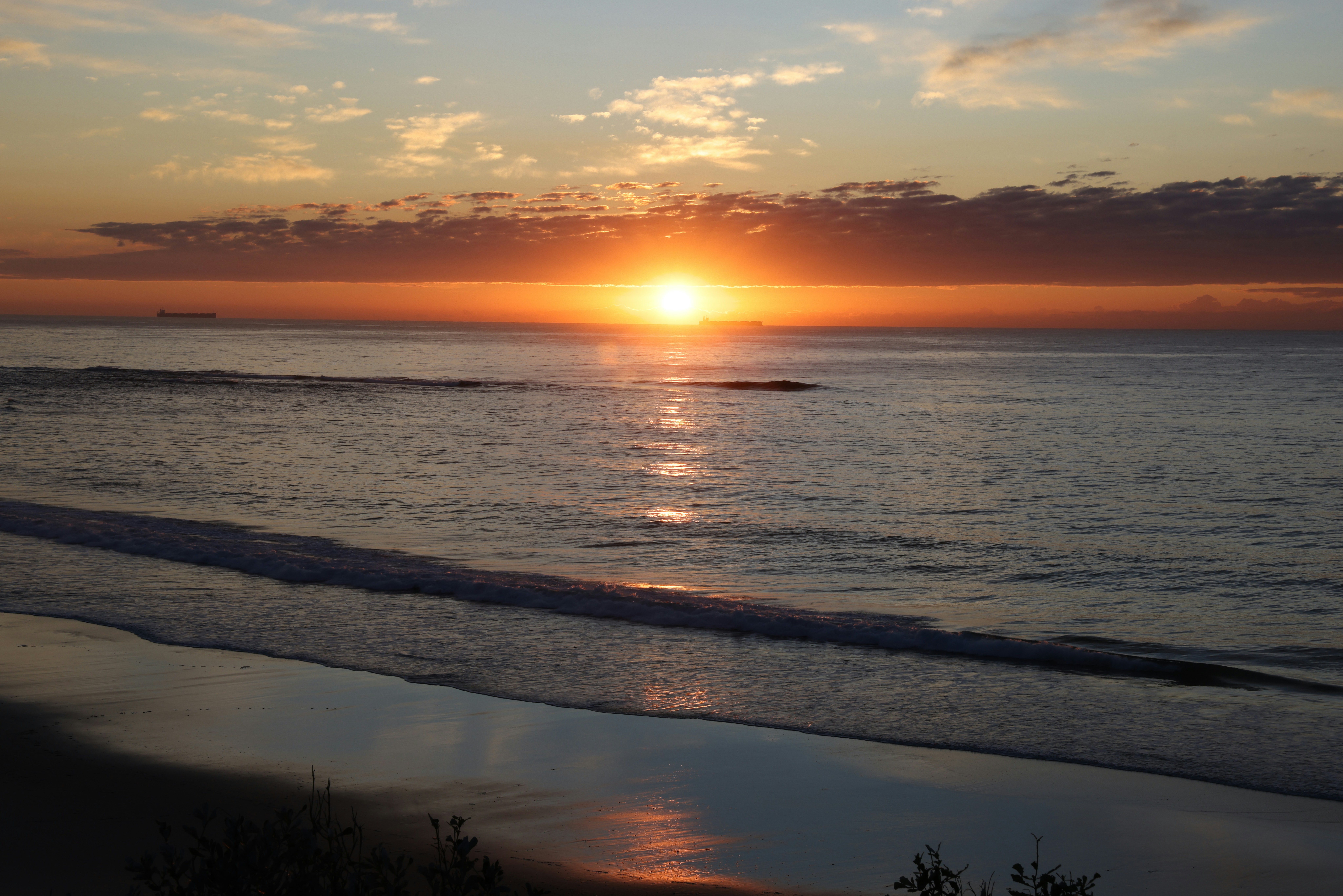 Sun rising over calm ocean waves with an orange horizon and scattered clouds.