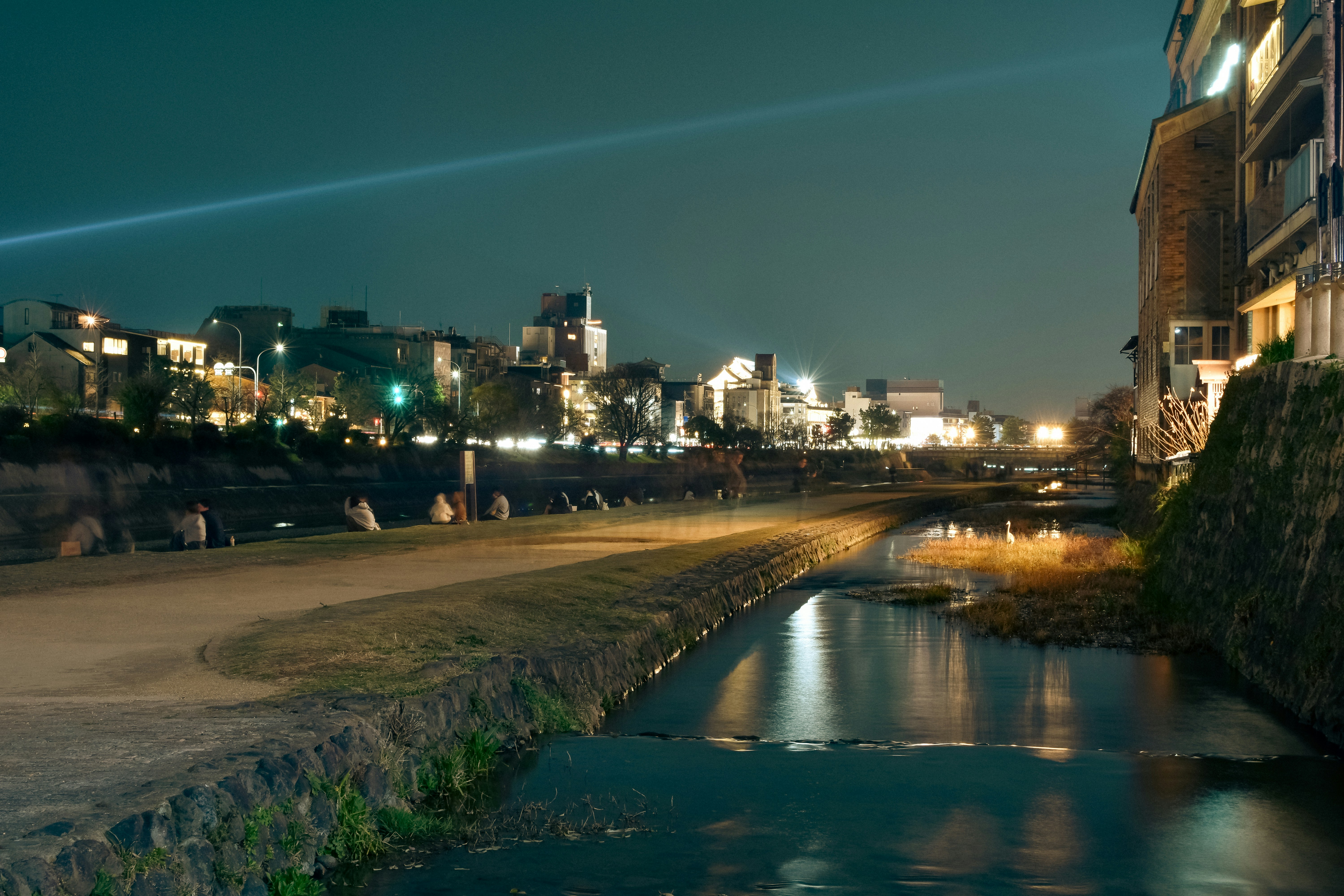 City skyline reflecting over a calm canal under a clear night sky.