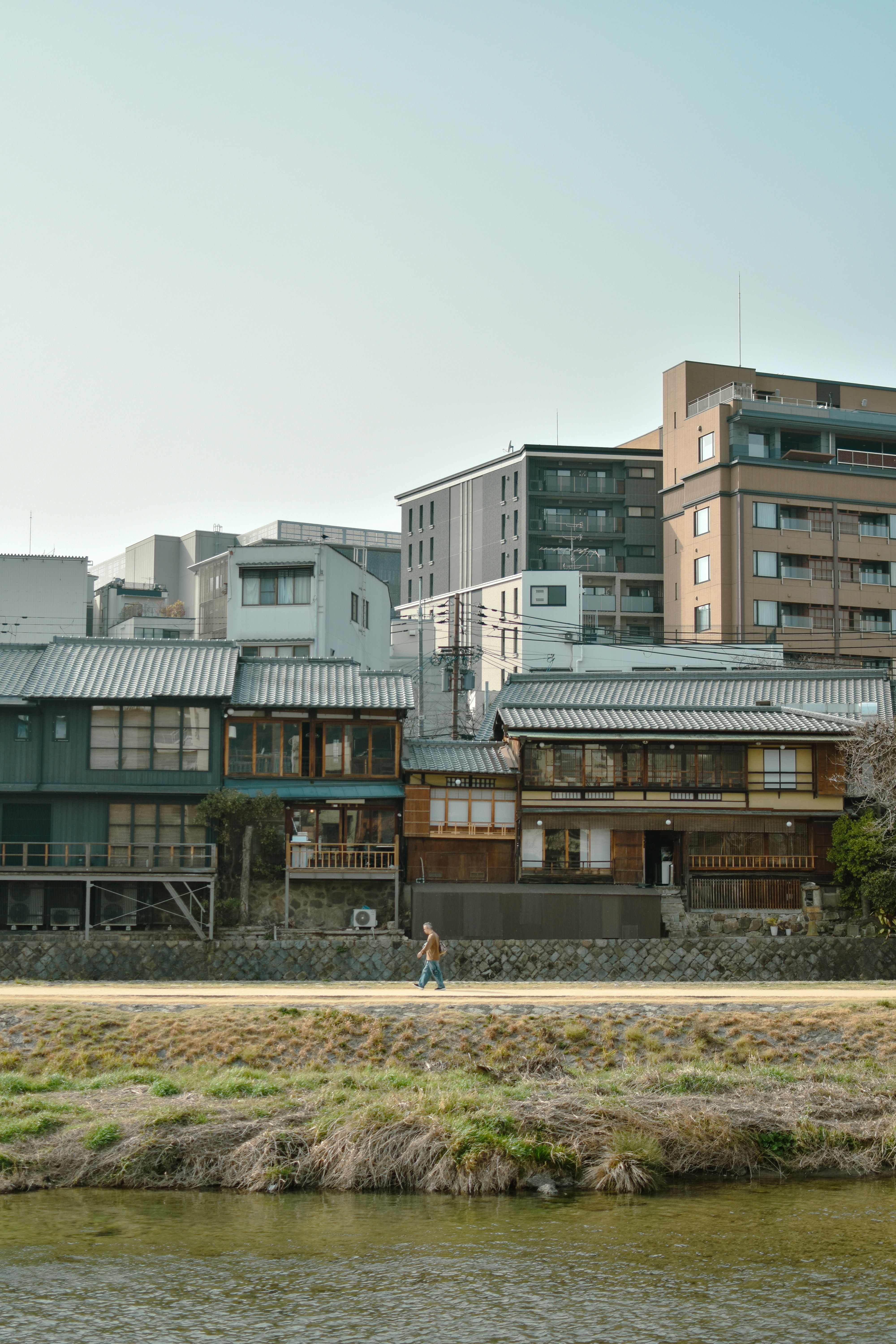 A serene riverside scene showcasing traditional wooden houses juxtaposed with modern buildings, reflecting the evolution of urban architecture.
