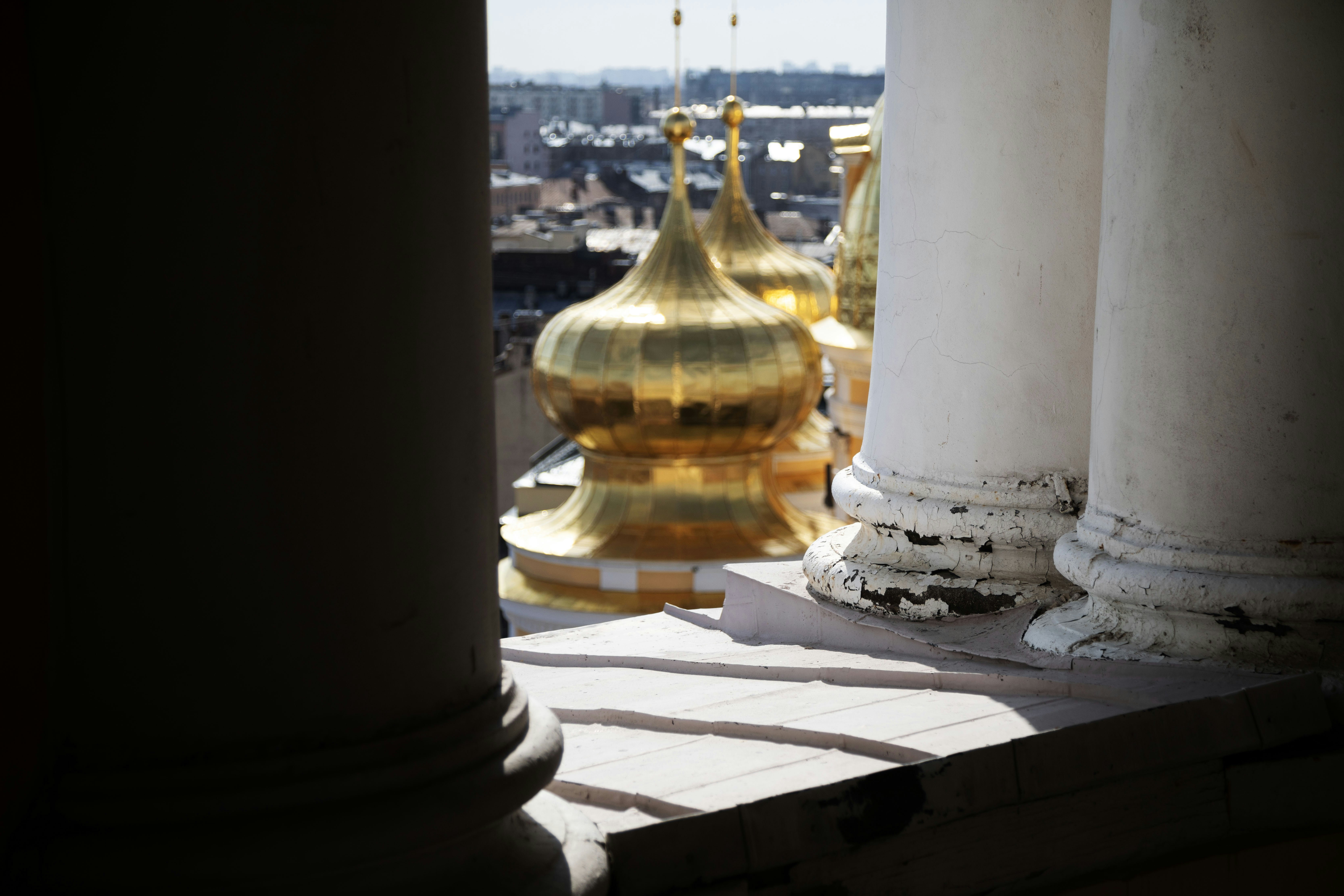 Golden domes of a cathedral peek through aged stone columns against a cityscape backdrop.