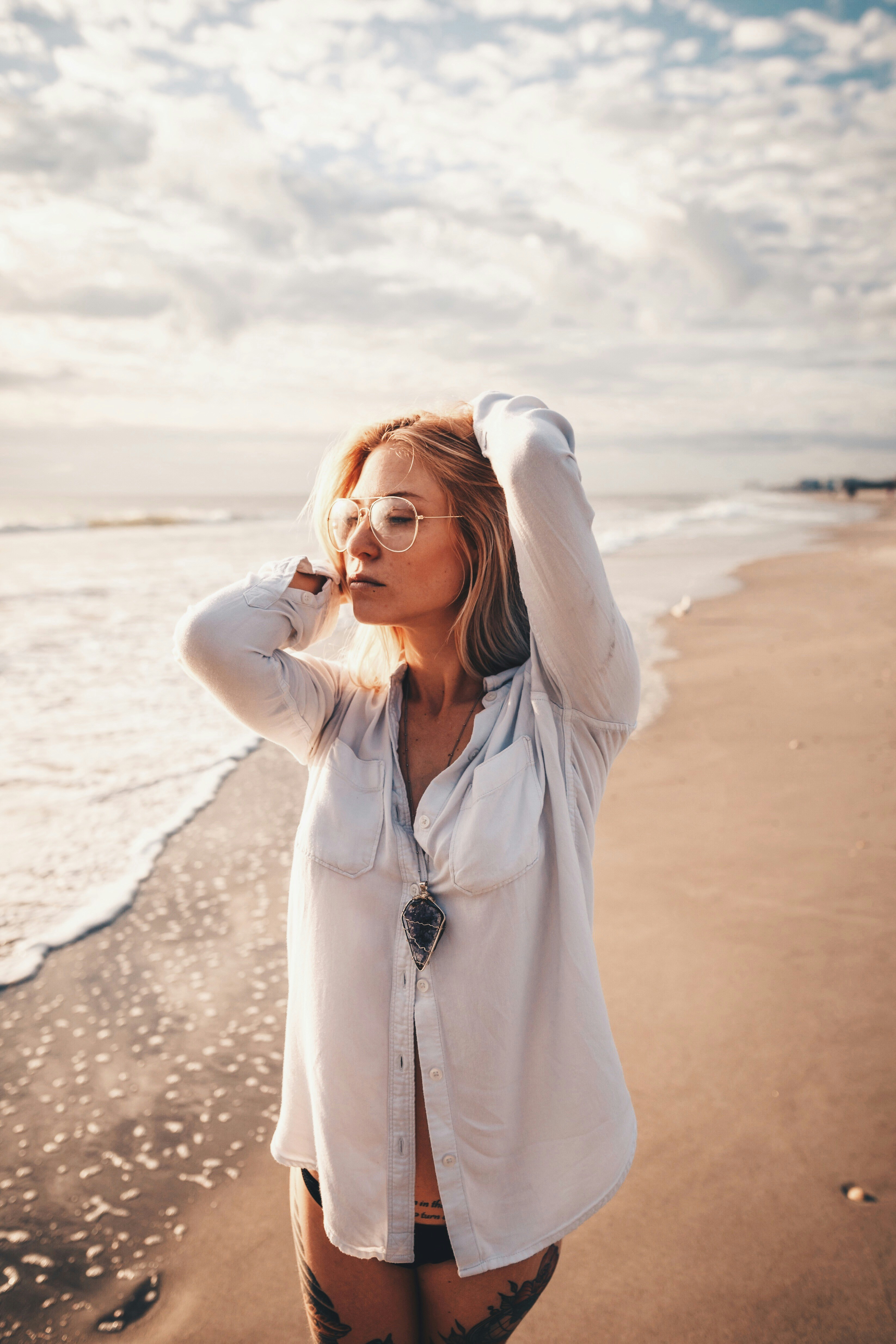 Person standing on sandy beach with waves and cloudy sky in background.