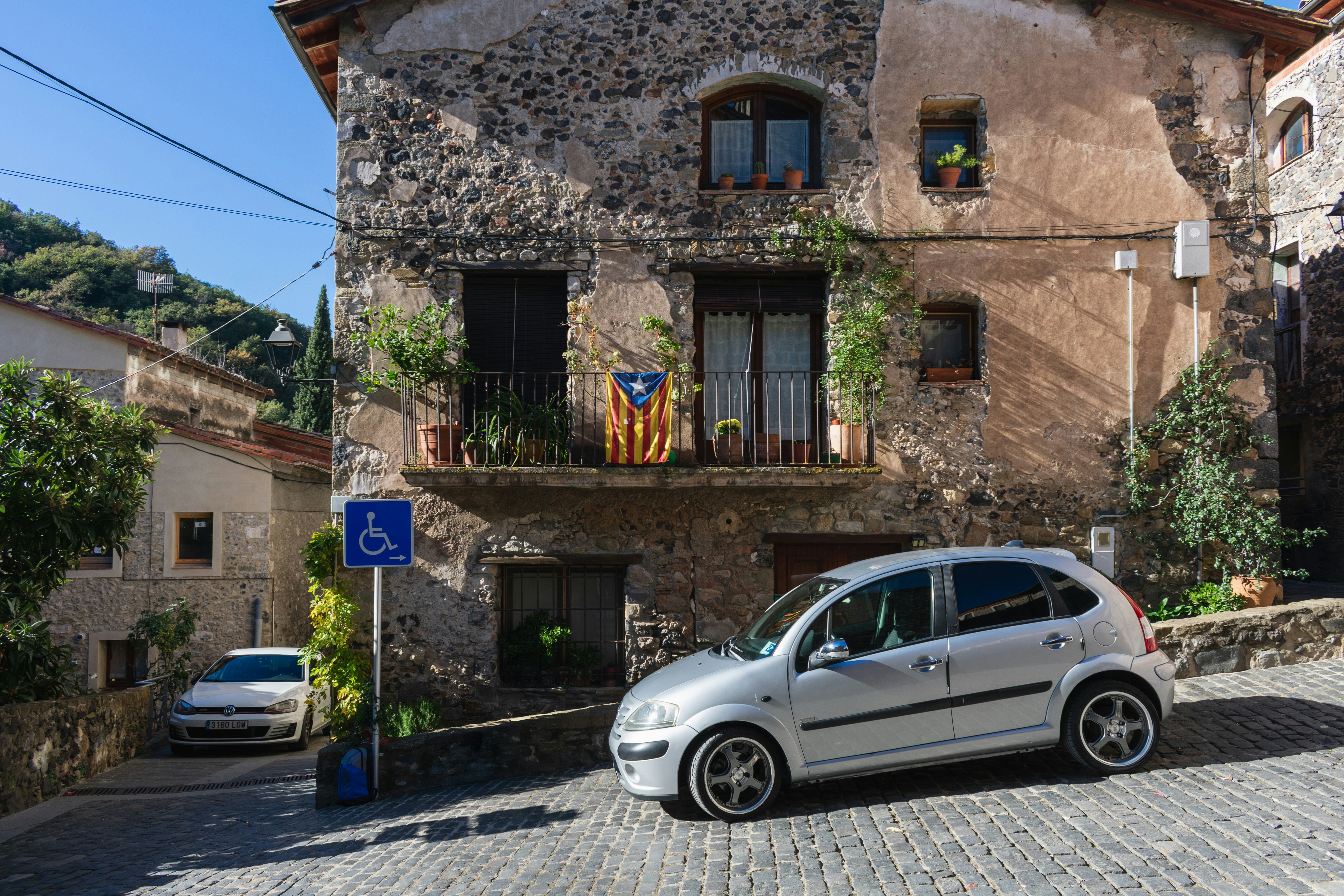 Stone house with rustic balcony and parked car on a cobblestone street.