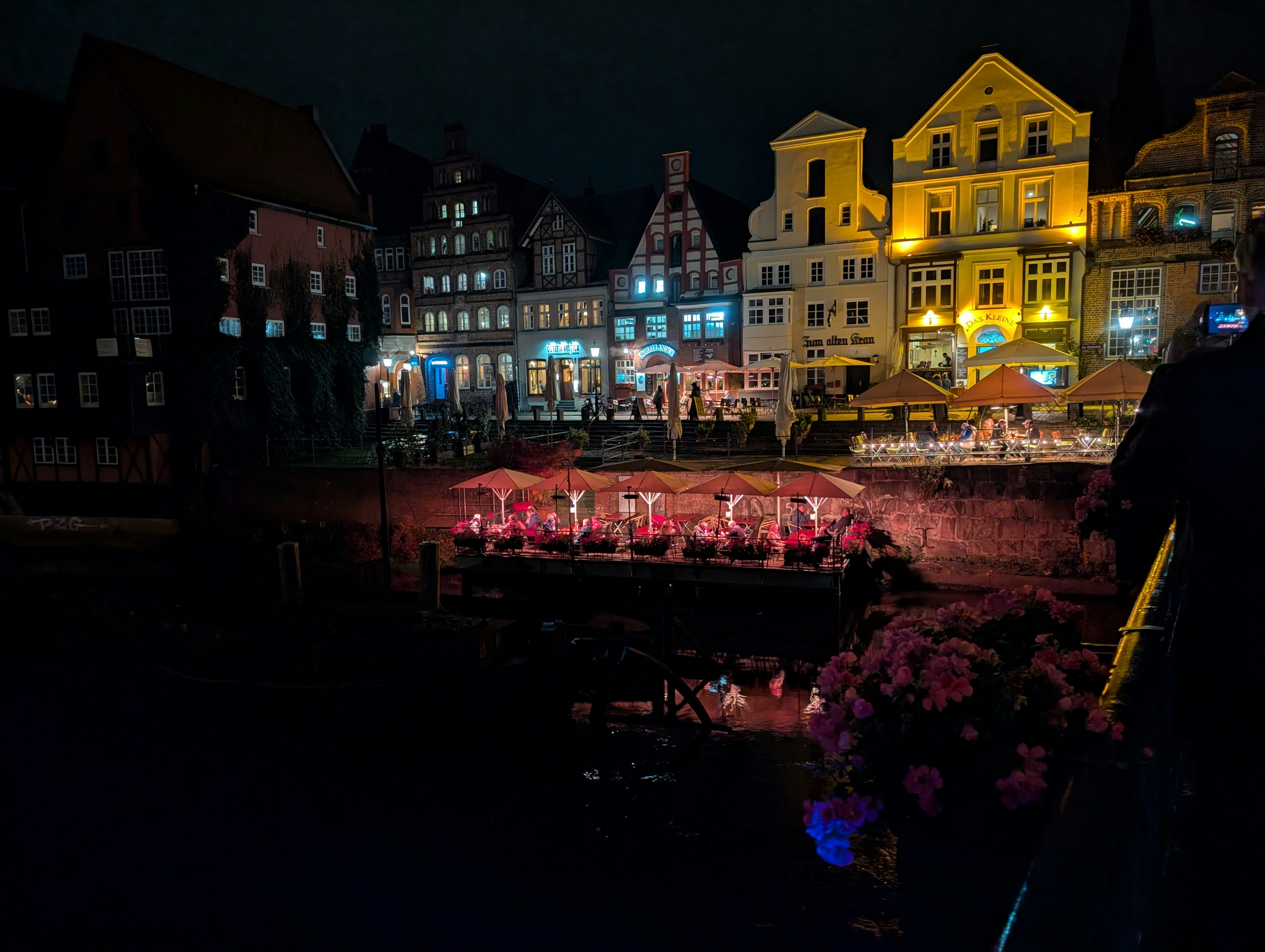 Historic half-timbered houses in Lüneburg illuminated with warm lights, reflecting on the riverside at night.